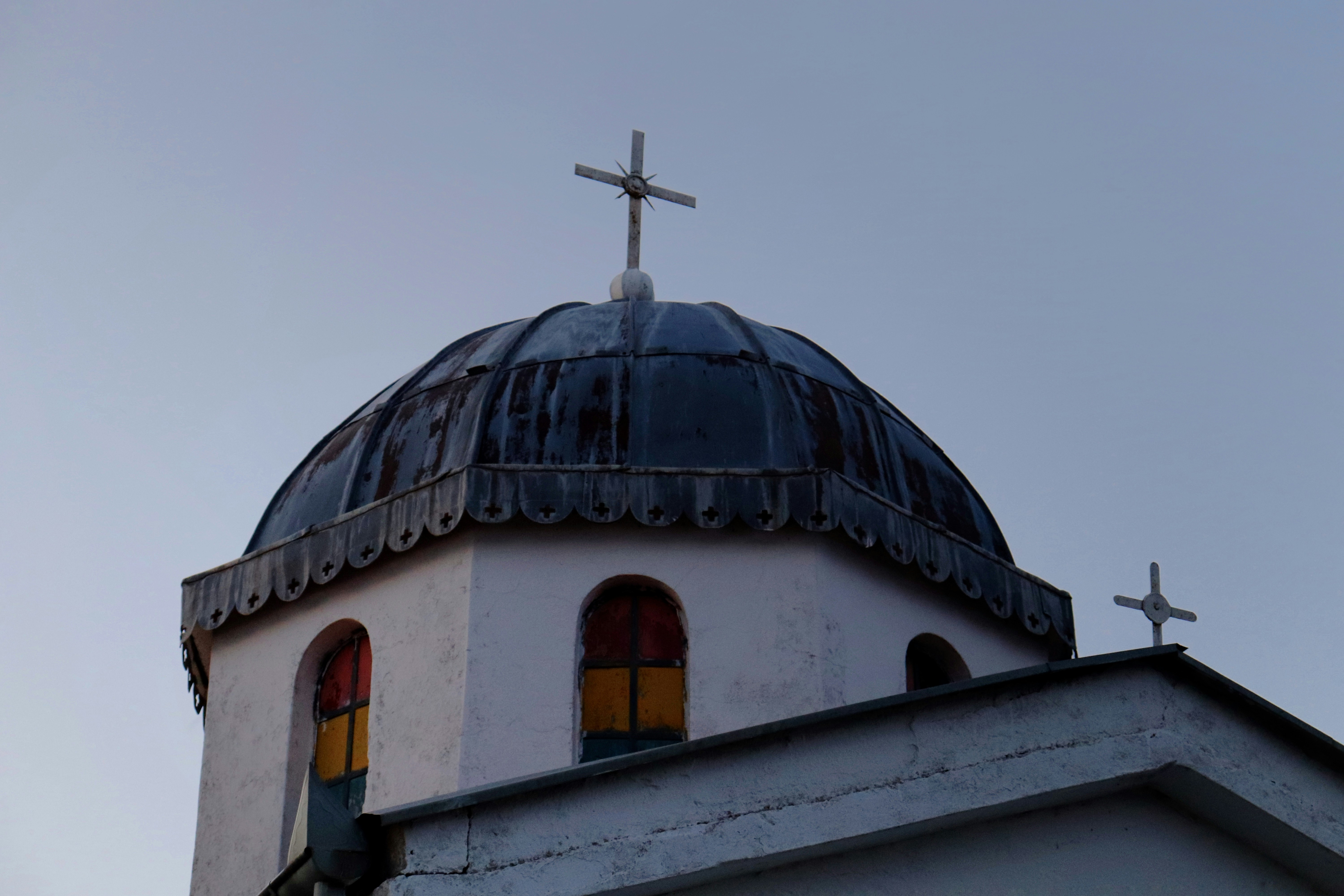 The ornate dome of a church, featuring colorful stained glass windows and a prominent cross, silhouetted against a soft evening sky.