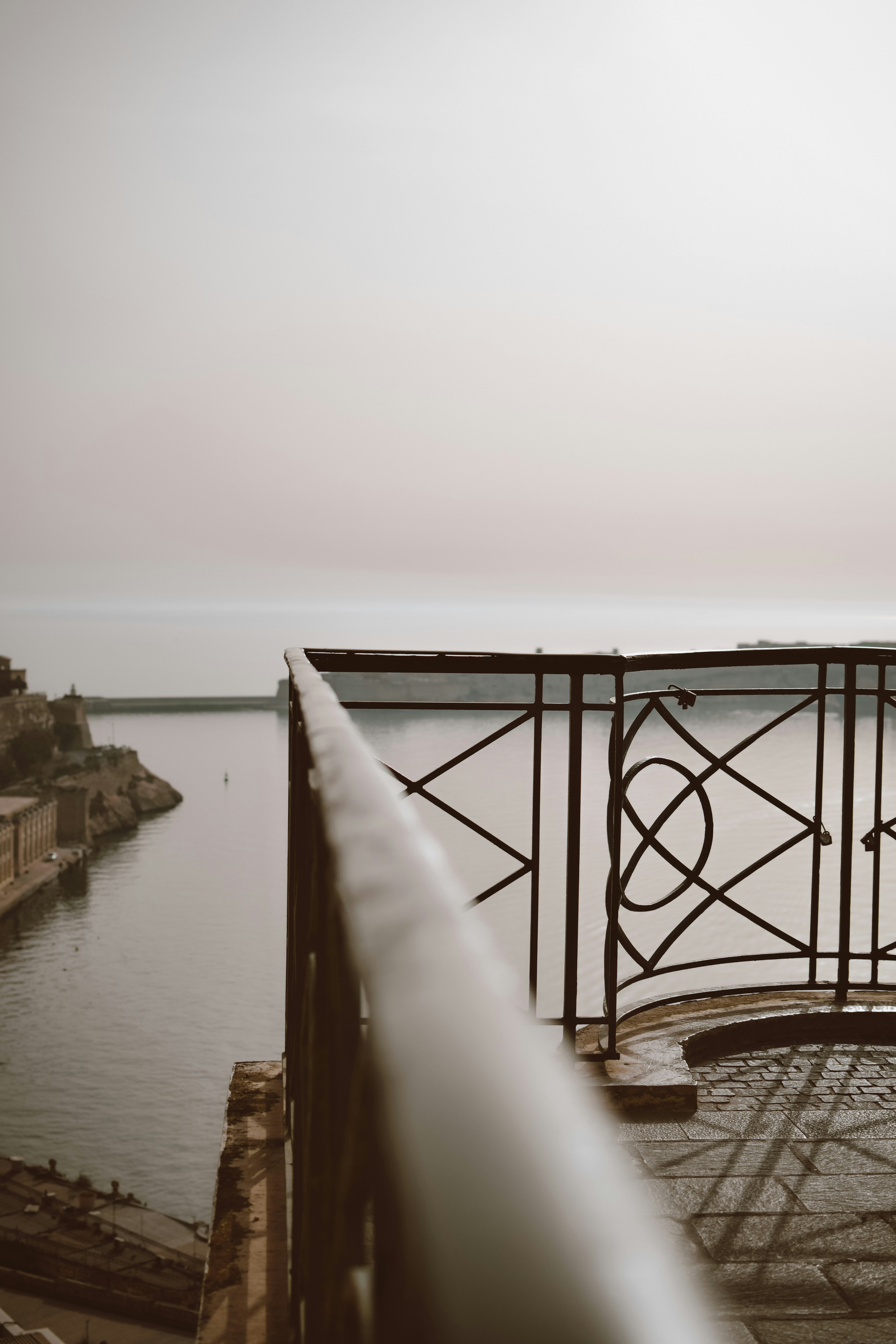 Intricate wrought iron railing frames a tranquil view of the waterway, with distant silhouettes of land meeting the horizon. 