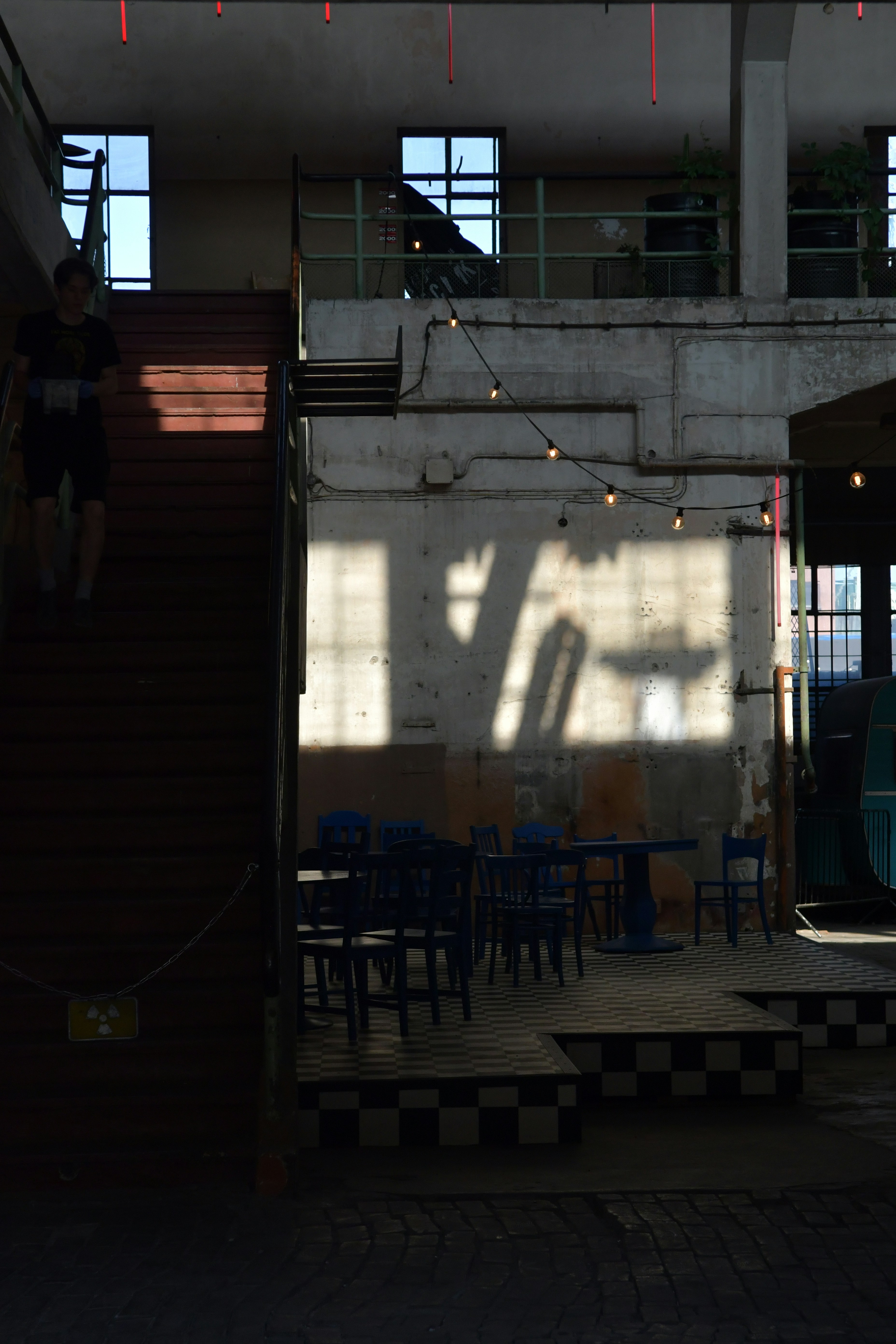 Industrial Café Atrium: String-Lights and Shadowed Staircase Over Blue Tables