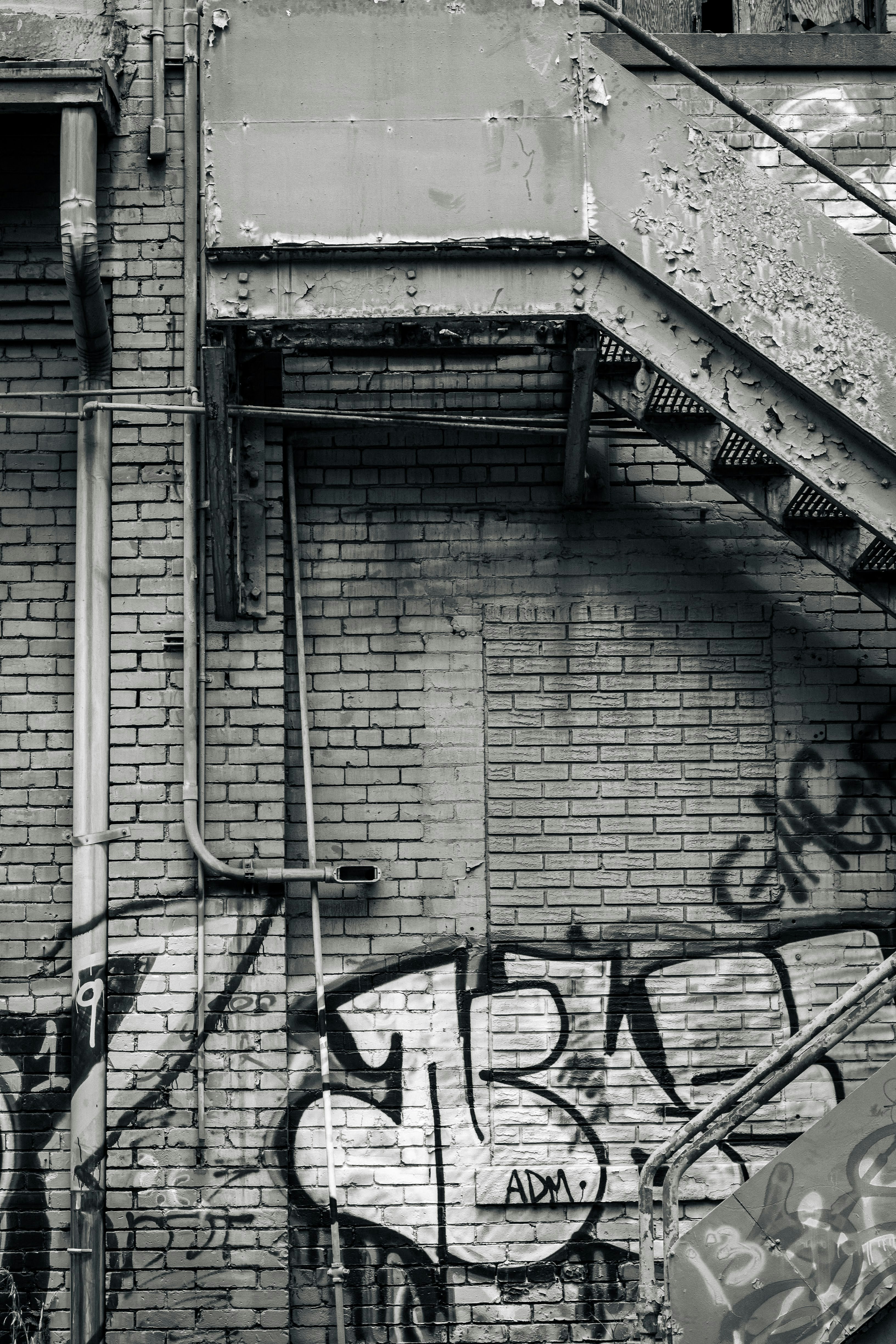 Weathered brick wall adorned with intricate graffiti and industrial piping, showcasing the intersection of art and decay.