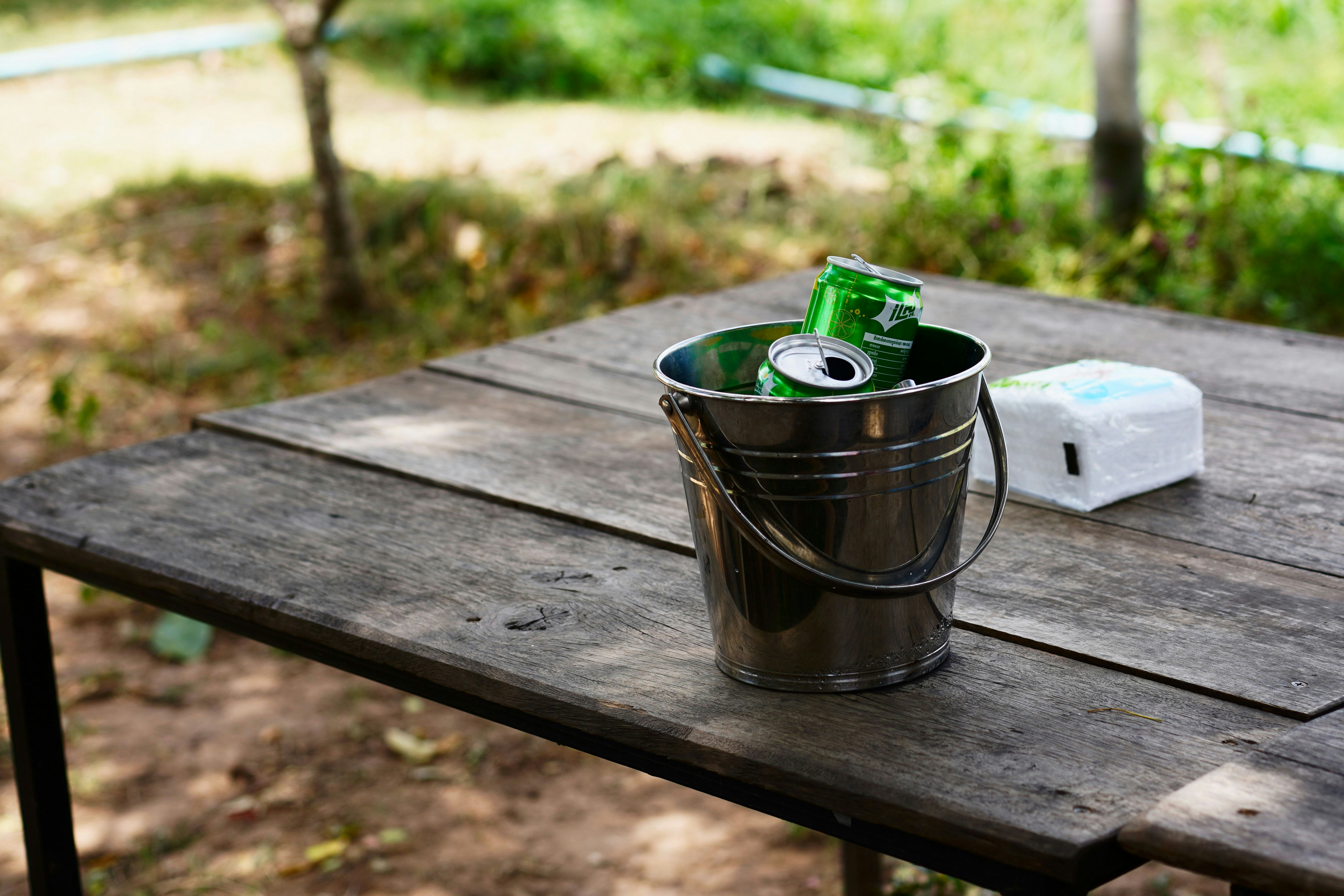 Steel can on a weathered wooden table under dappled park light