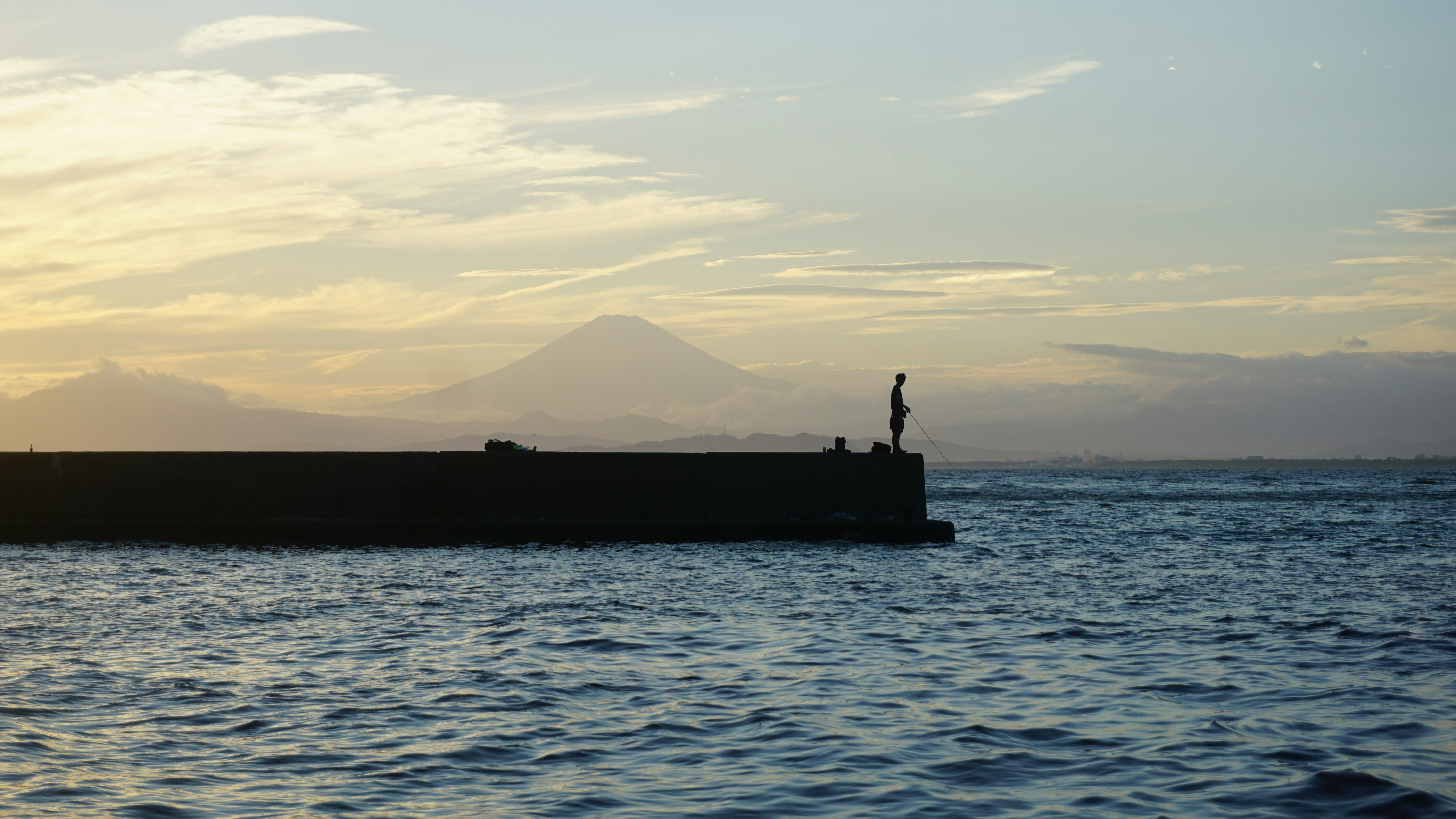 Dusk on the Jetty: A Lone Figure Against a Distant Snow-Capped Peak