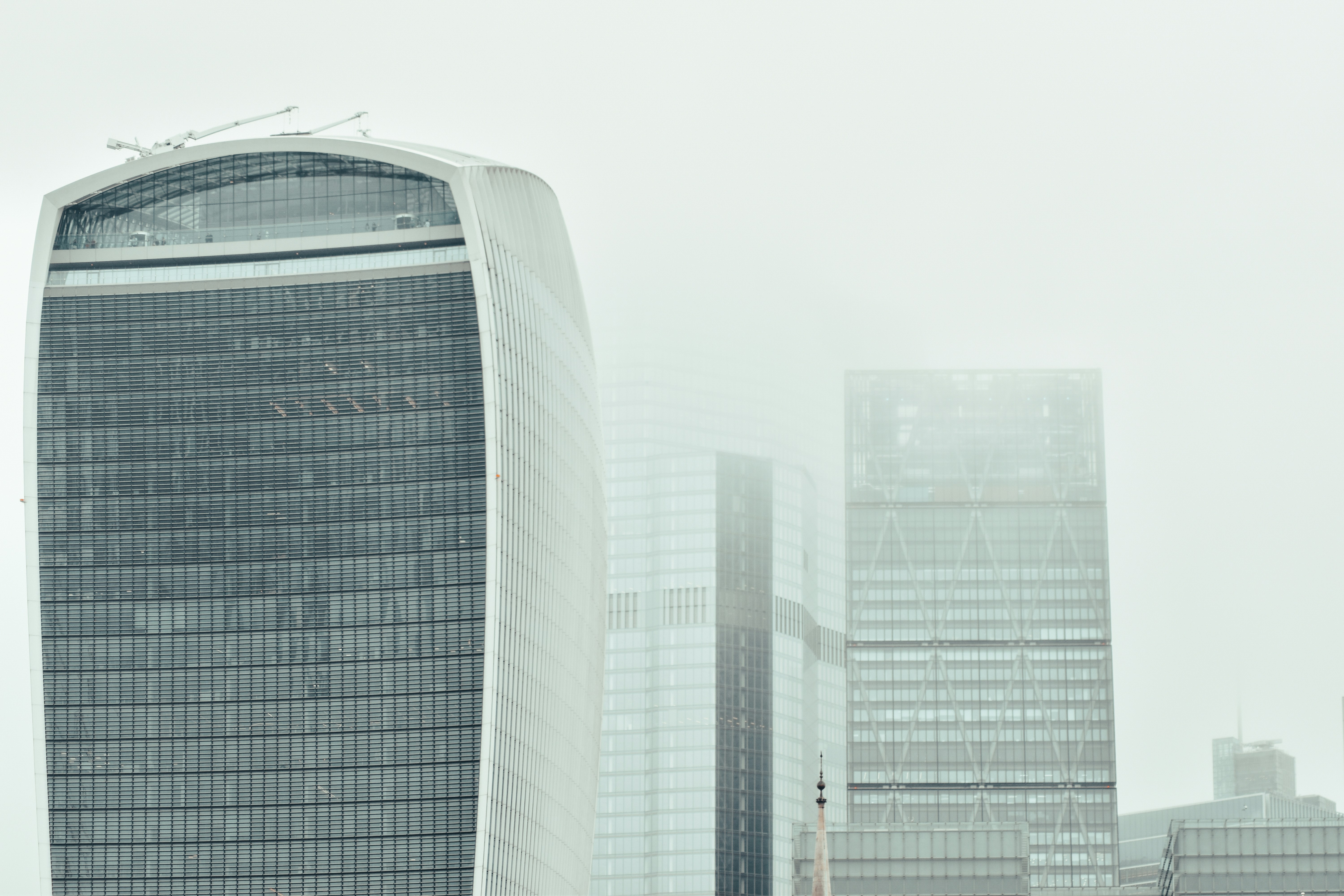 Modern skyscrapers shrouded in fog, showcasing unique architectural designs against a muted sky.