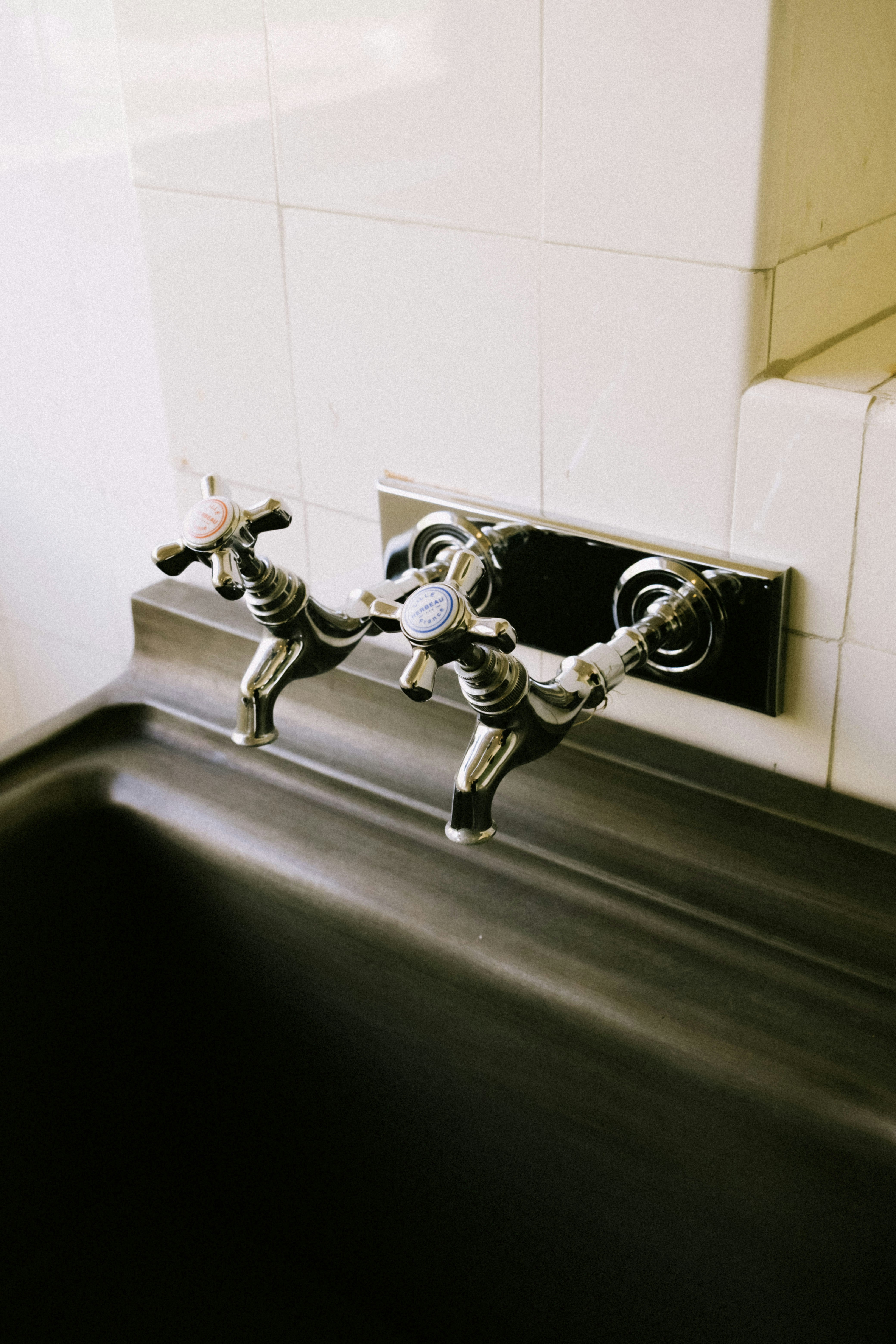Close-up of chrome faucets with red and blue handles mounted above a stainless steel sink, showcasing a blend of vintage design and modern utility.
