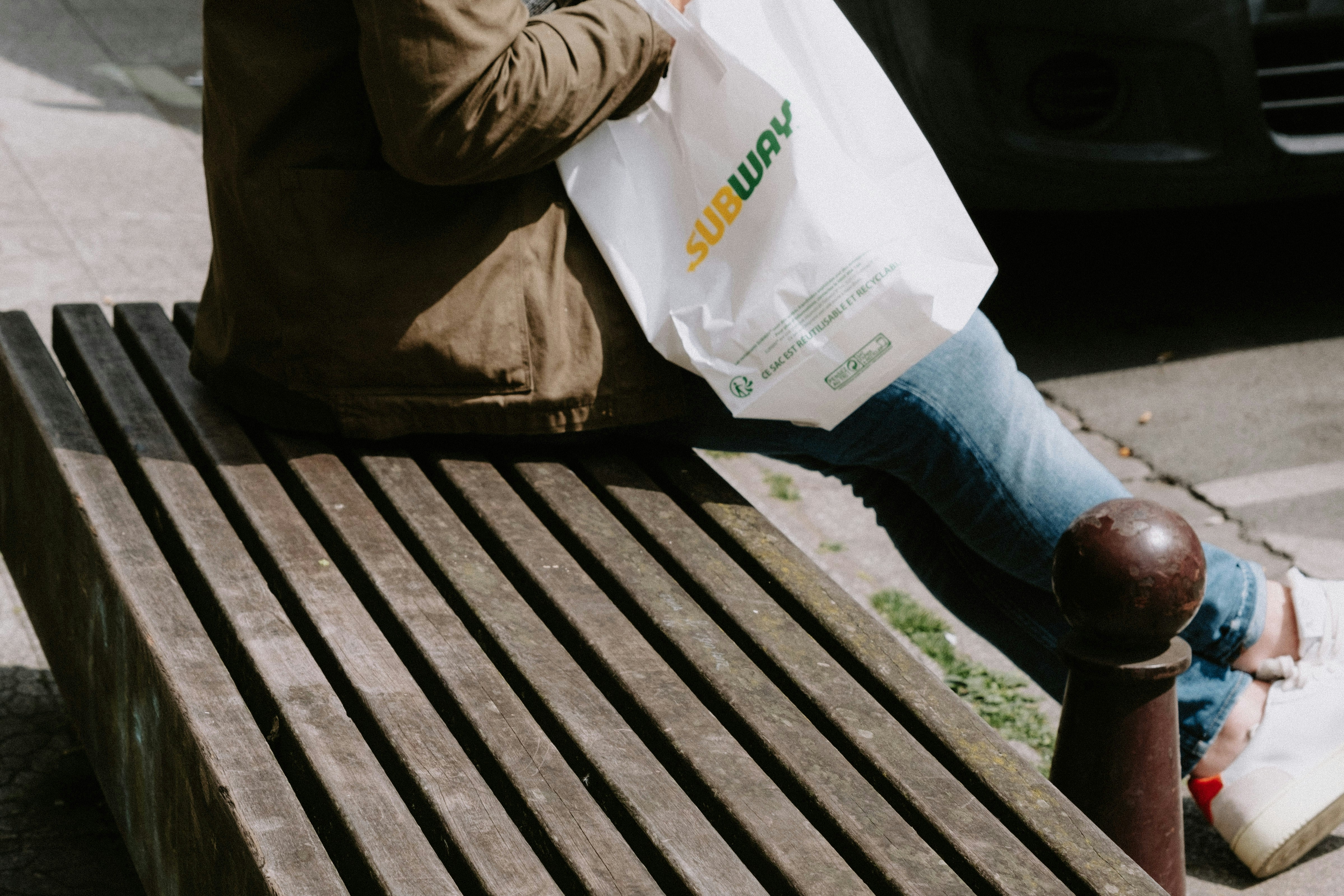 Person sitting on a wooden bench holding a branded food bag.