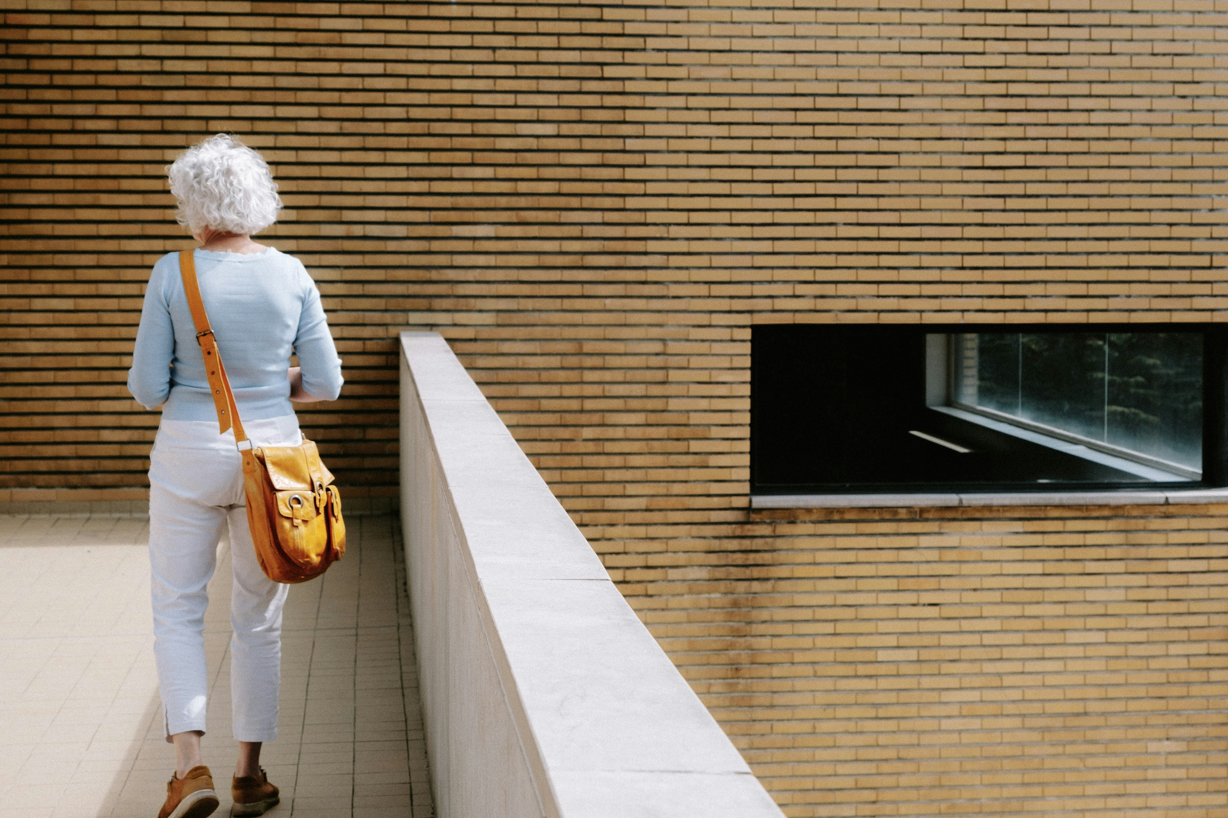 An Elderly Traveler with an Amber Messenger Bag Traverses a Brick Terrace