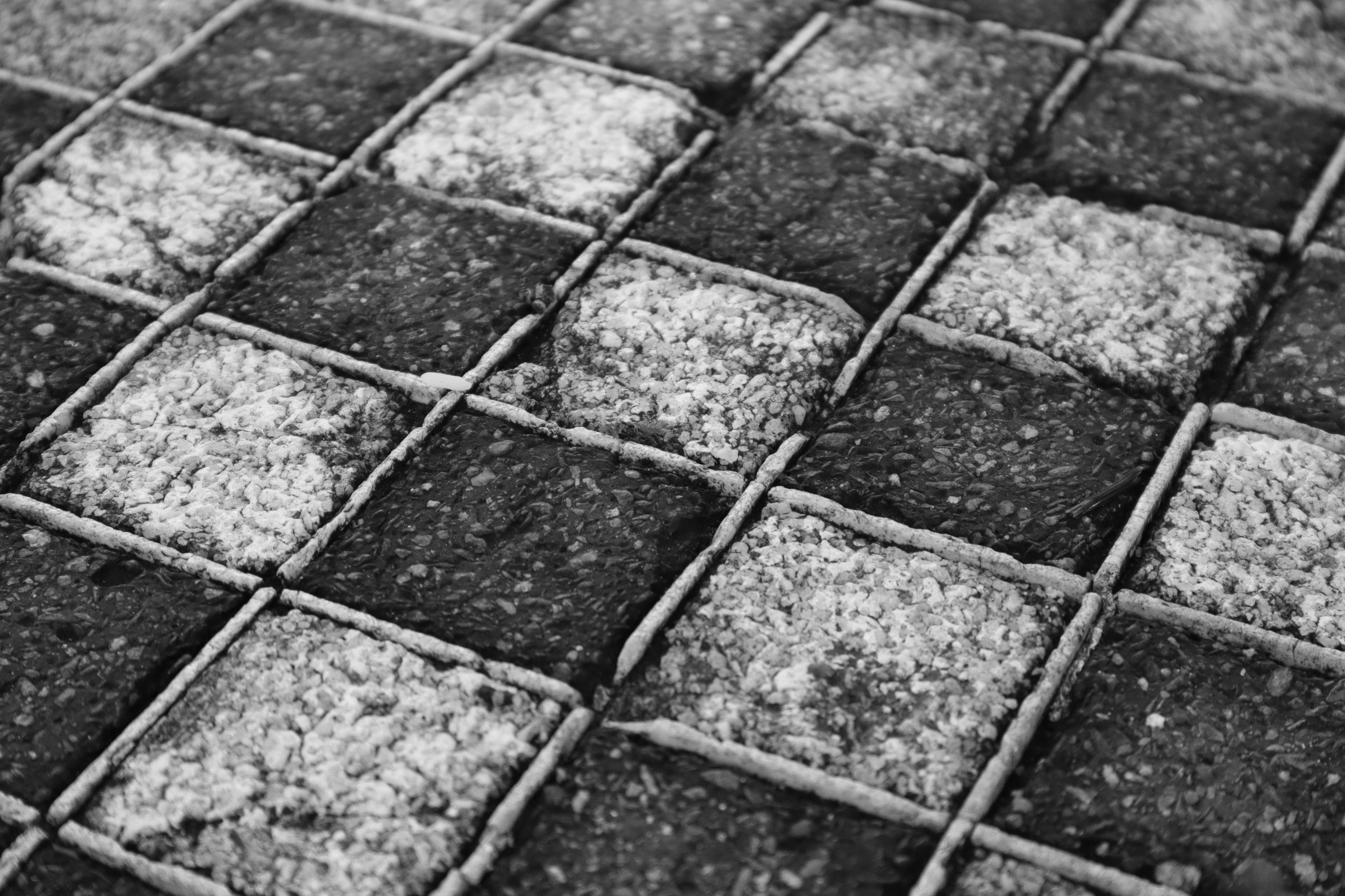 Close-up of a weathered checkerboard-style pavement in black and white.