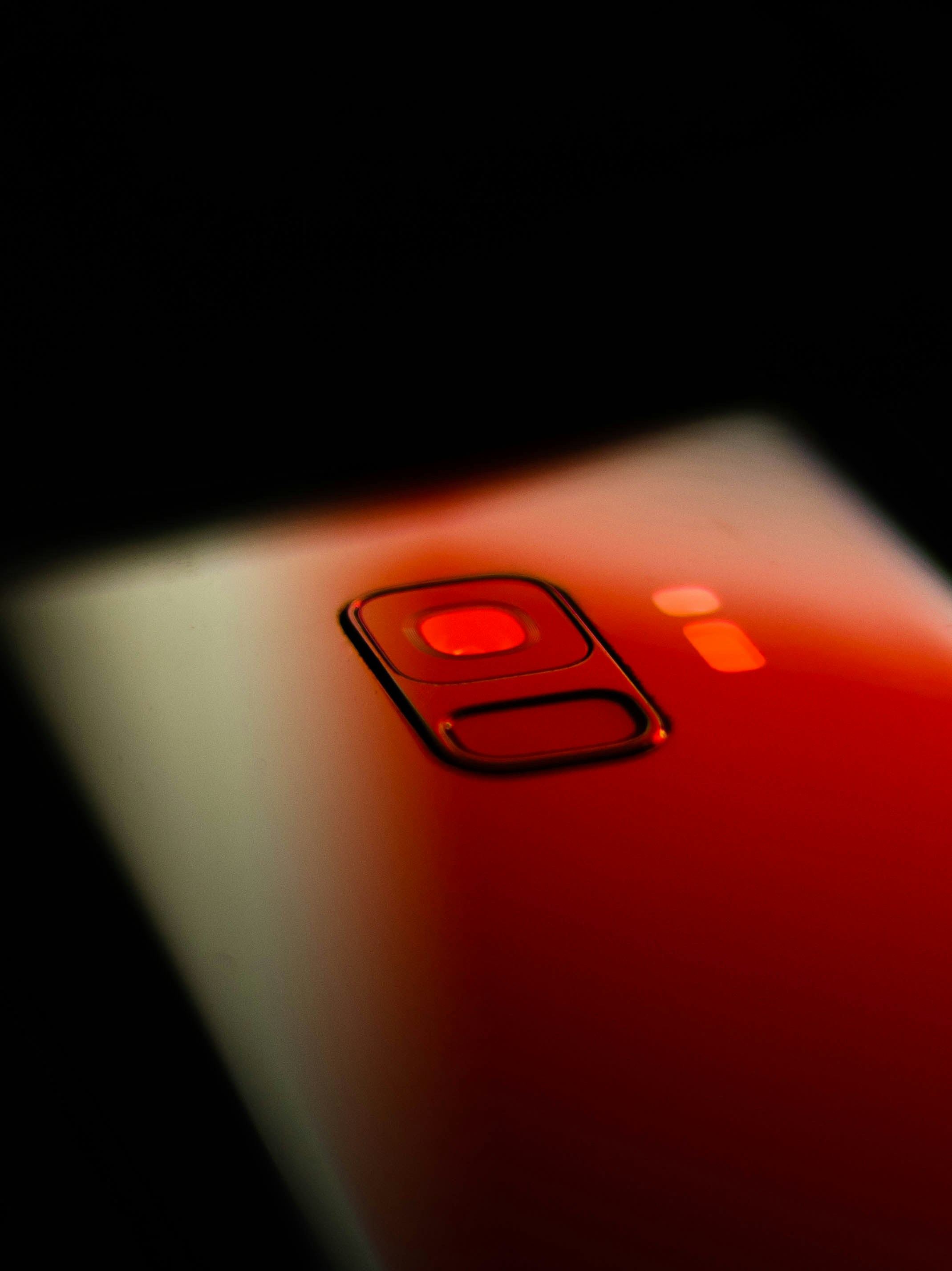 Close-up of a smartphone's rear camera module illuminated by a soft red light, showcasing sleek design and detail.
