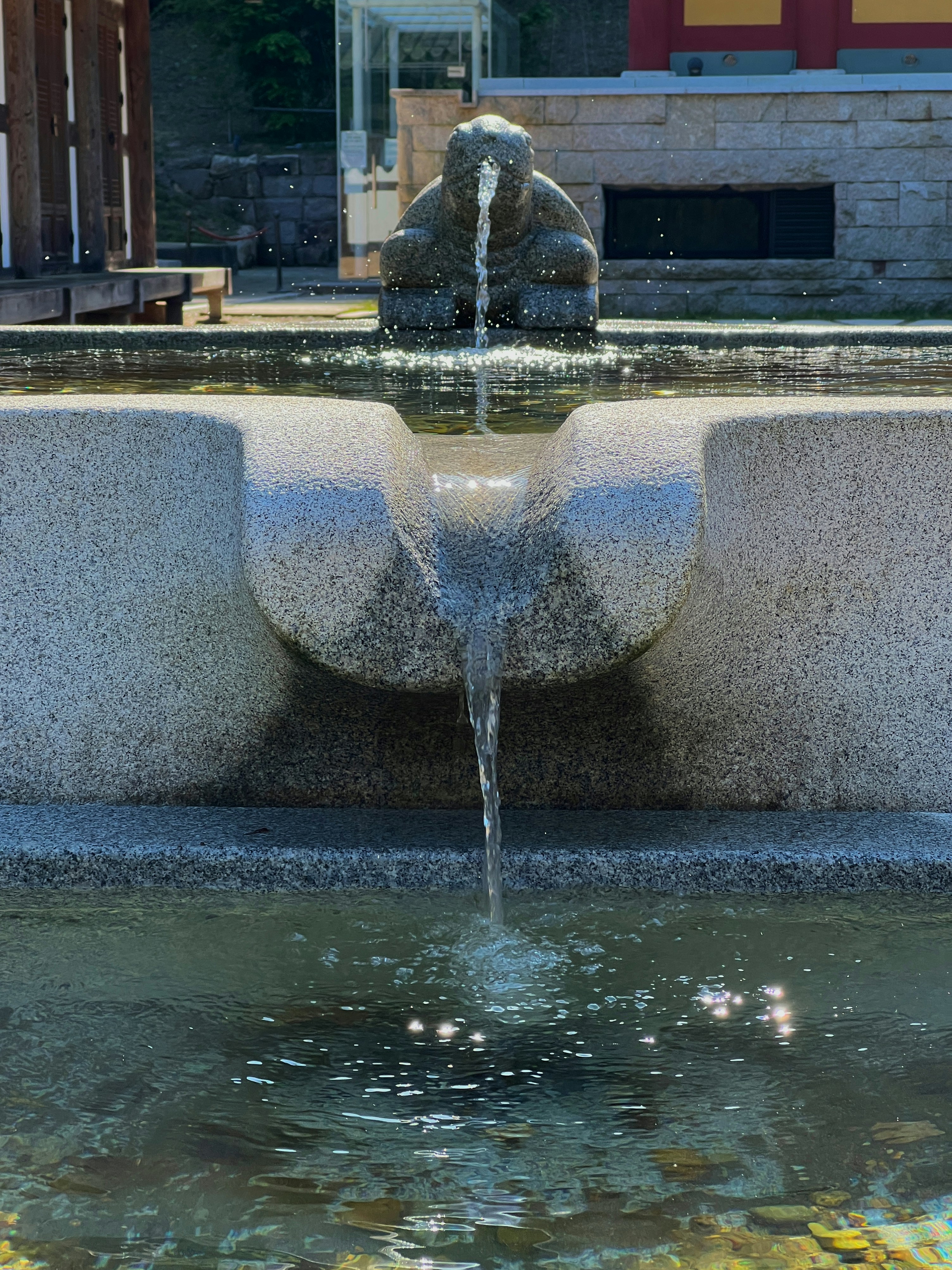 A serene water feature with a sculpted stone figure spouting water, surrounded by a reflective pool. The interplay of light and water creates a tranquil atmosphere.