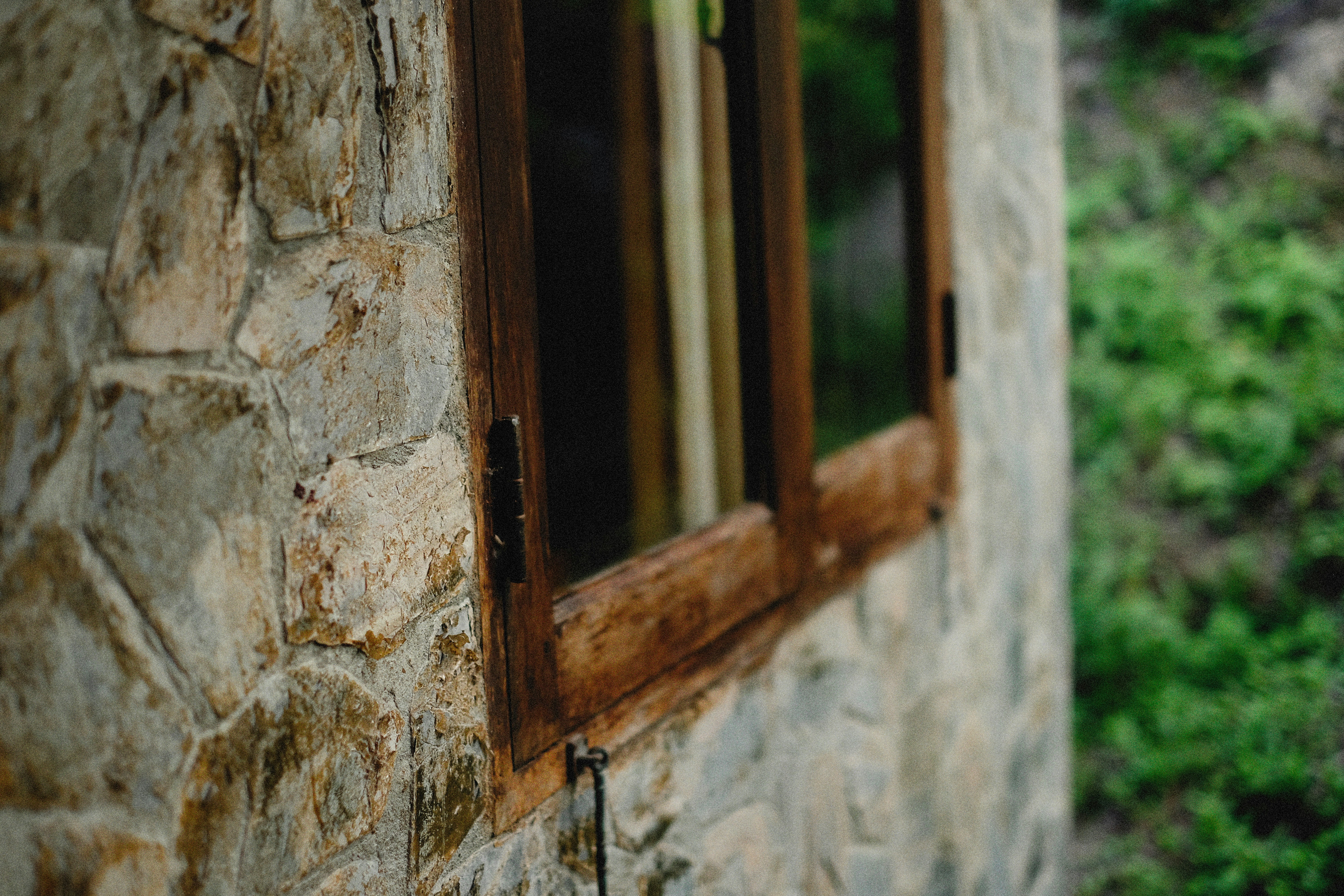 Weathered stone wall with wooden window frame, surrounded by lush greenery.