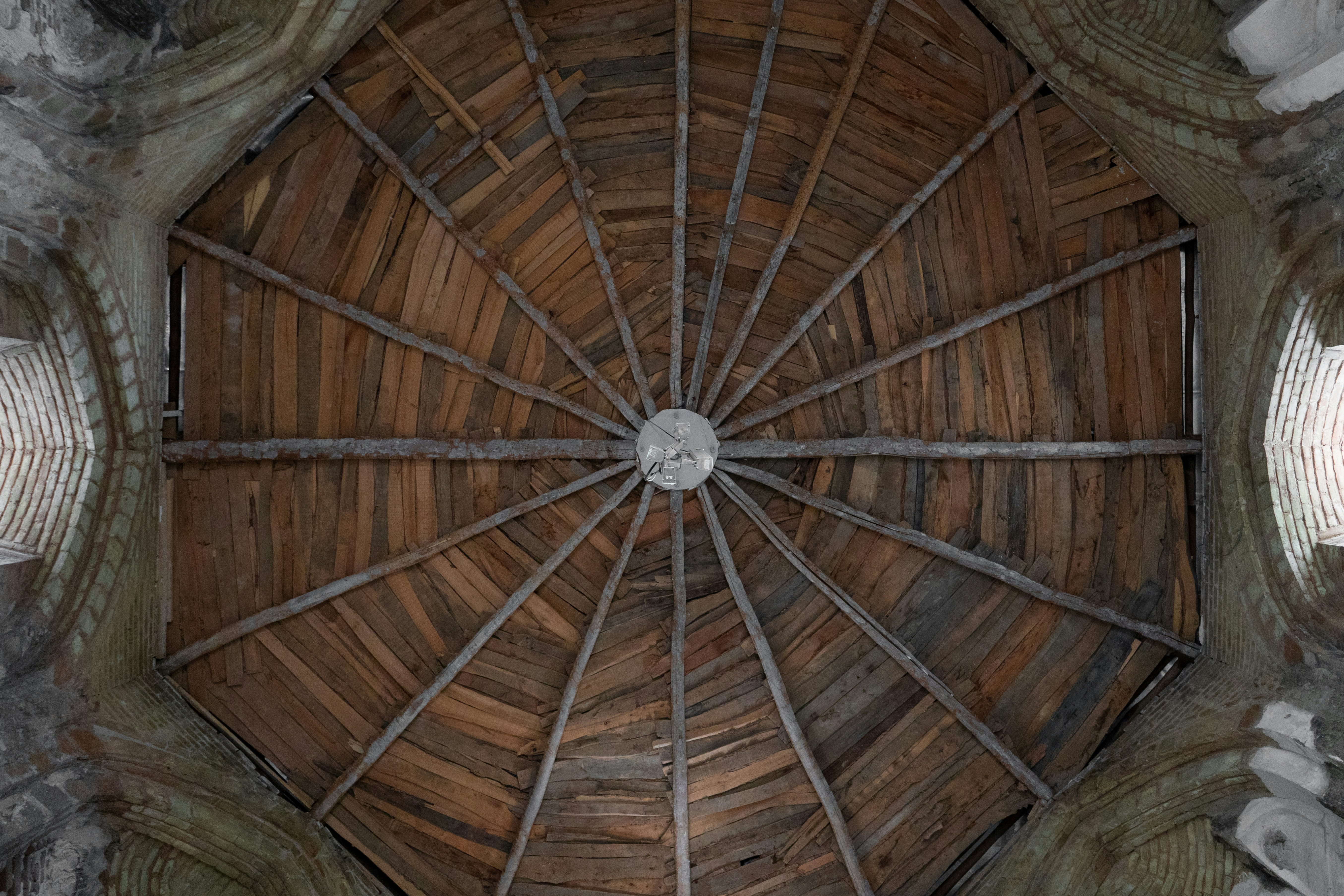 Intricate wooden ceiling structure viewed from below, showcasing radial beams and a central hub. The craftsmanship highlights the architectural beauty of the space.