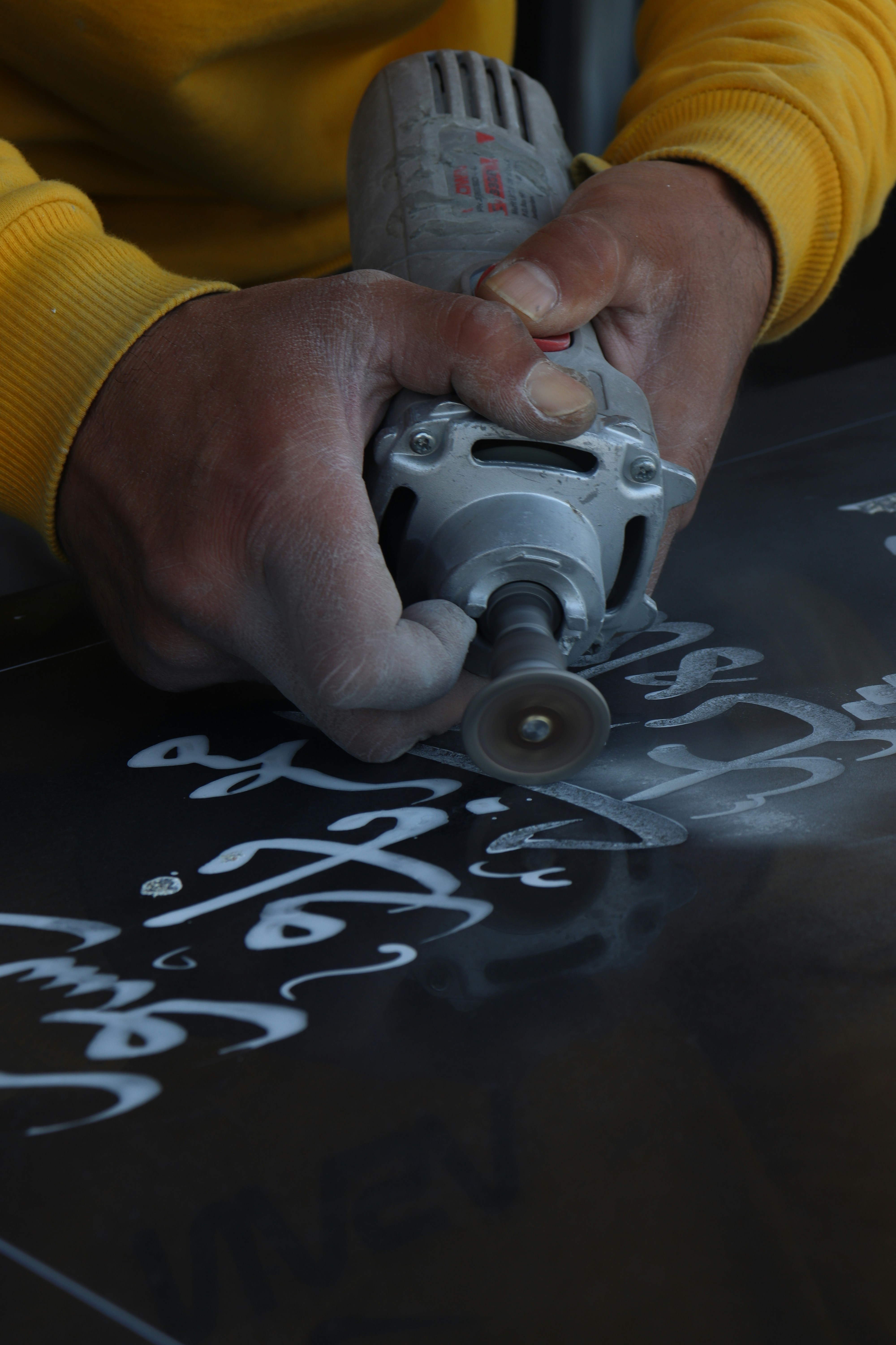 Grinding the Script: A Craftsman's Hands Shape White Lettering on Dark Metal