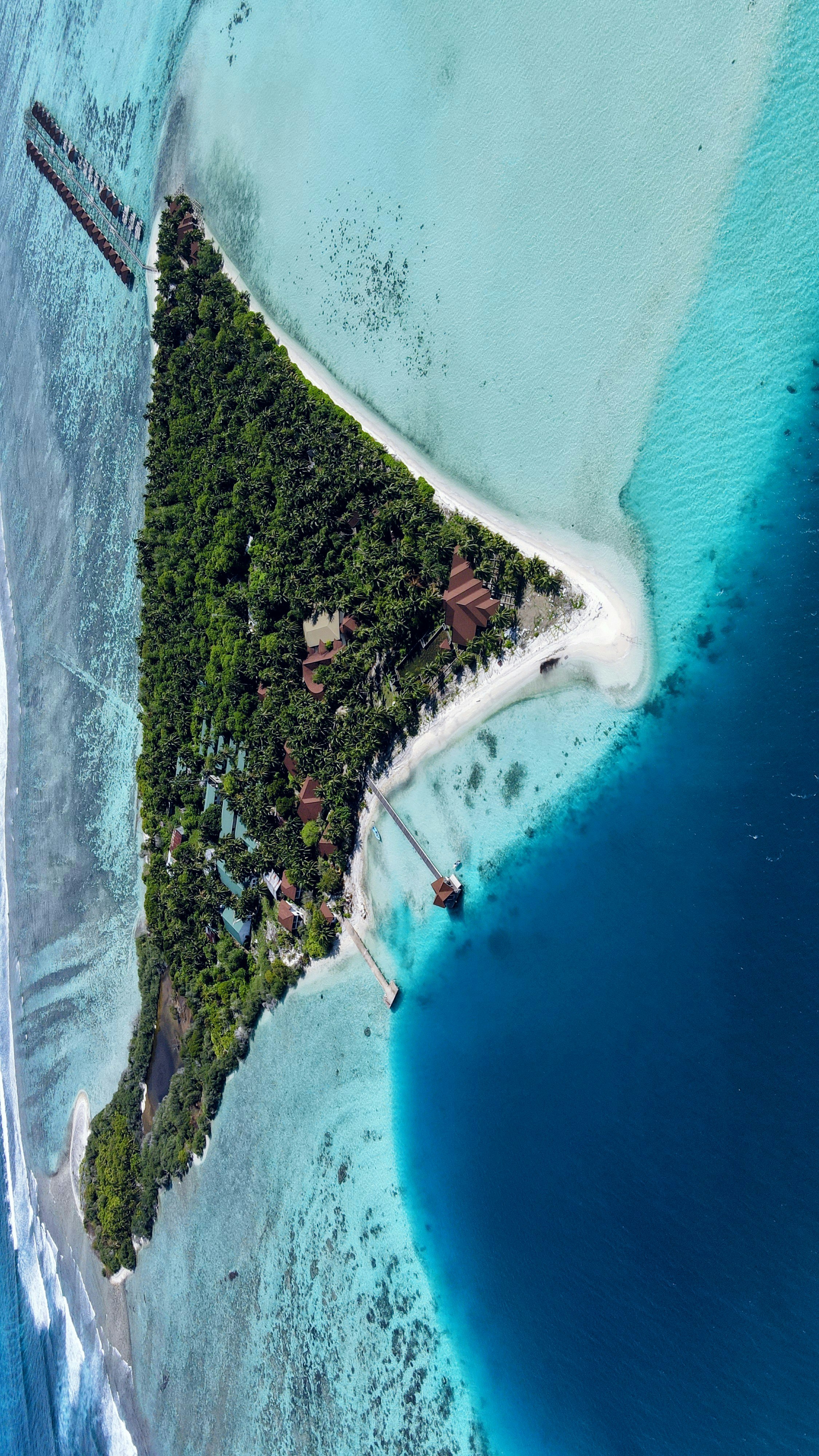 Aerial view of a lush, green island surrounded by vibrant turquoise waters, showcasing a blend of nature and luxury accommodations.