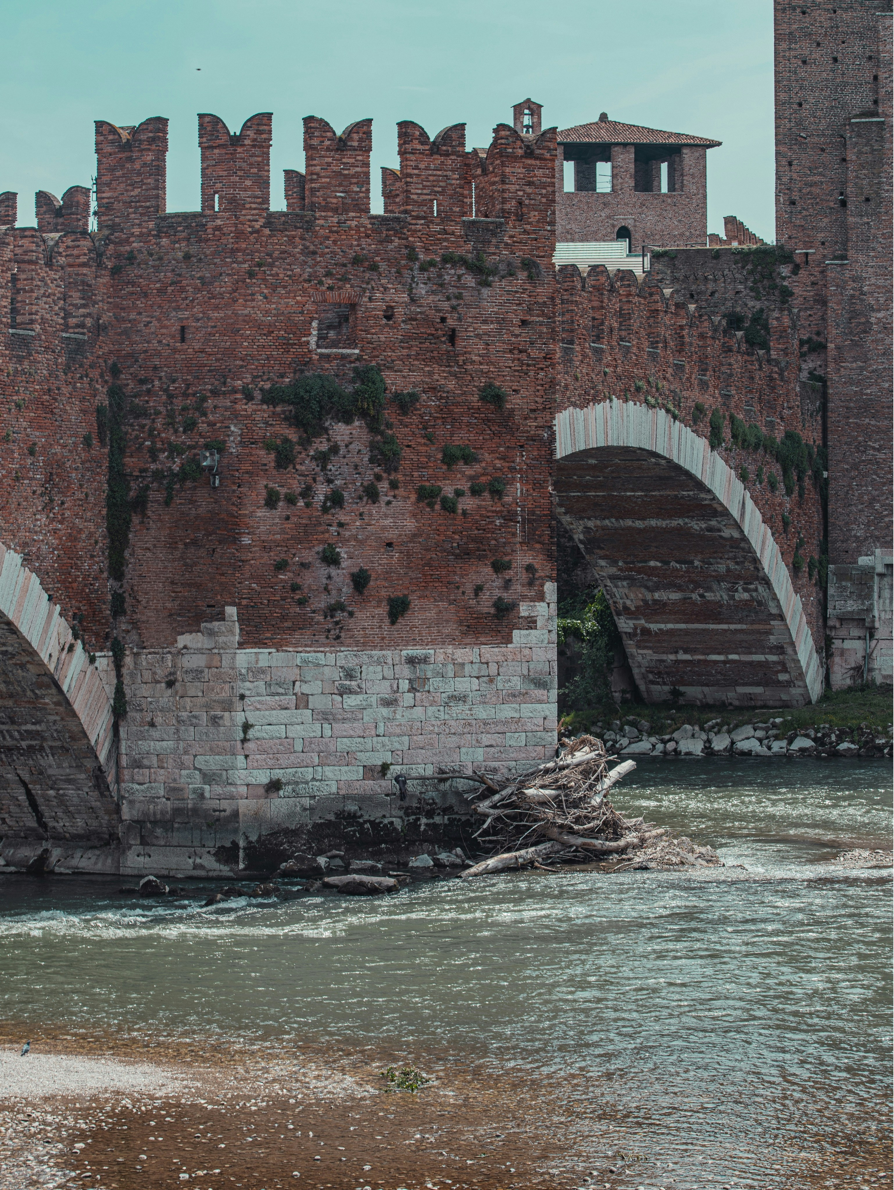 Ancient stone bridge adorned with historical architecture, partially submerged in a flowing river, surrounded by lush greenery.