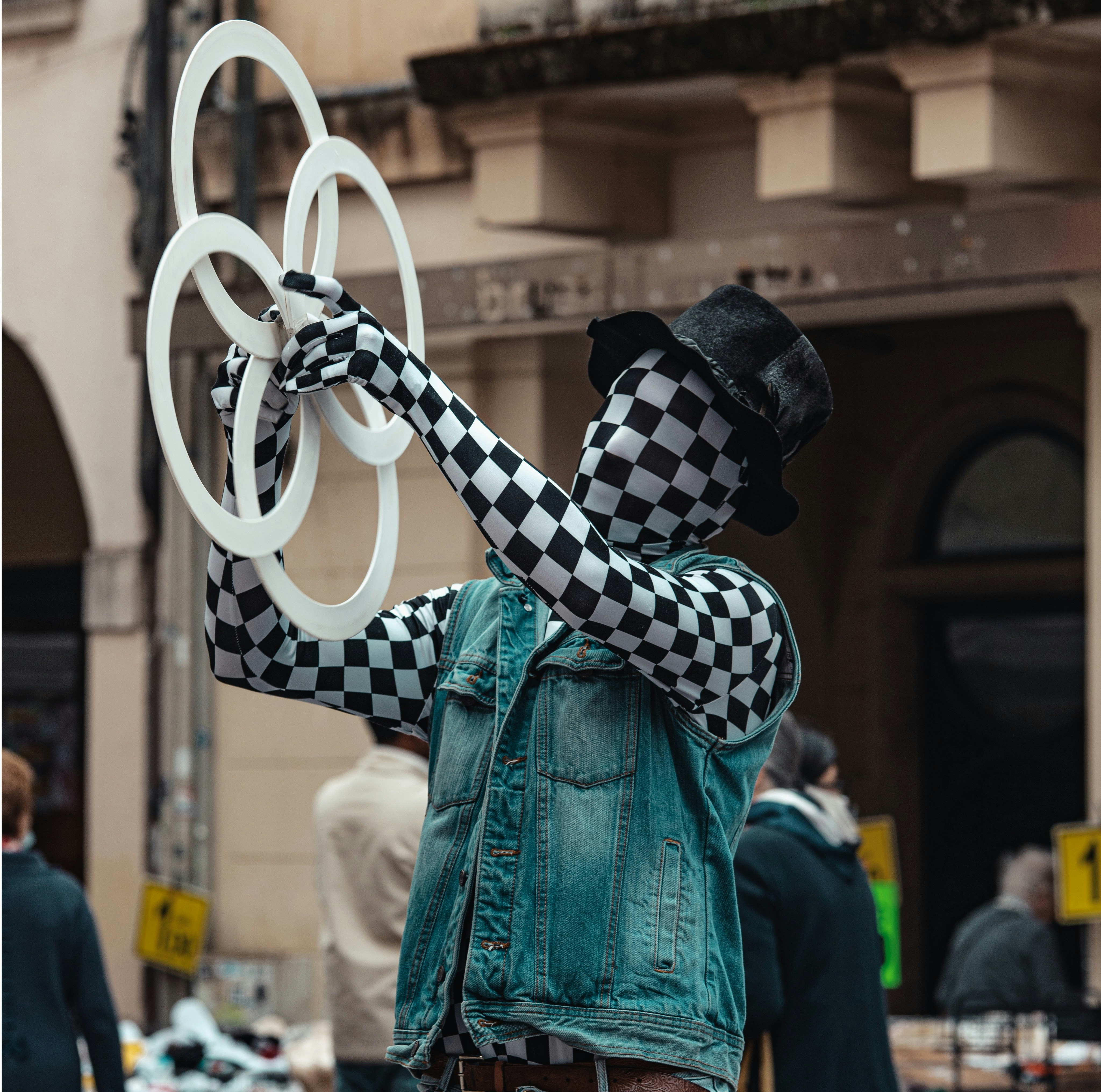 Street performance featuring a checkerboard-clad figure manipulating large circular props in front of an urban façade.