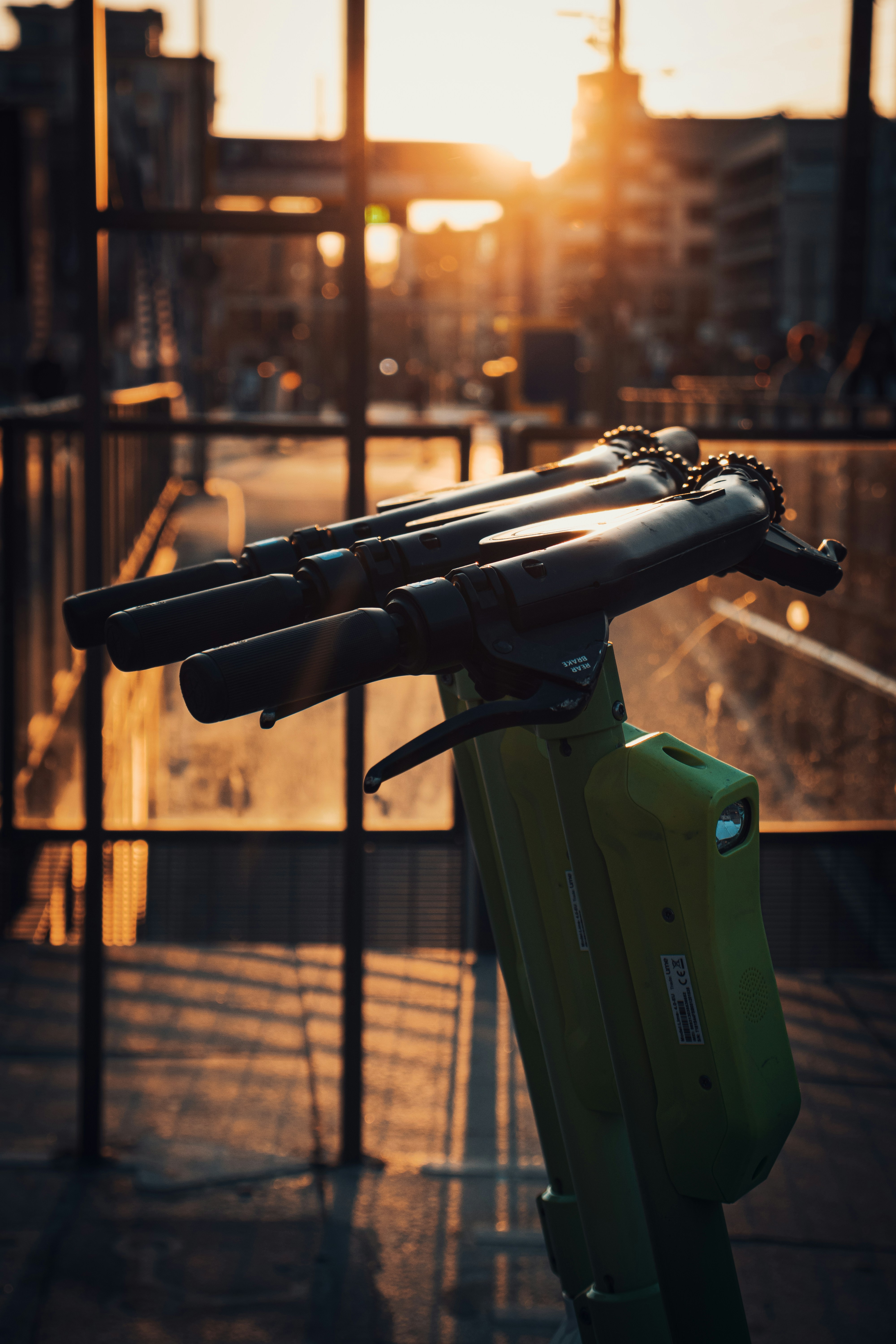 Electric scooters lined up against a backdrop of a glowing sunset, casting long shadows on the pavement.