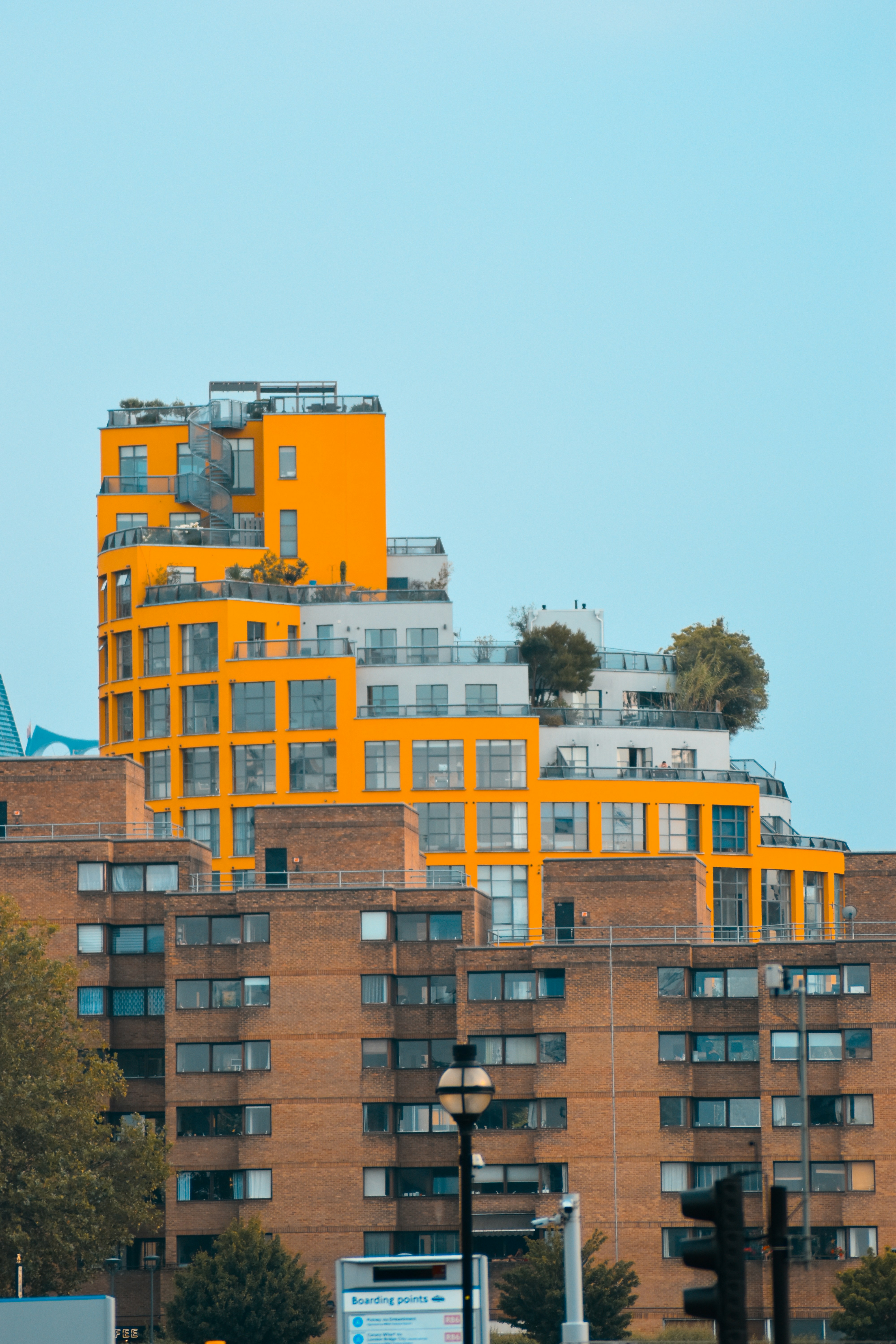 A modern building with vibrant orange facades and lush greenery on terraces, contrasting against a clear blue sky. The structure showcases innovative urban design.