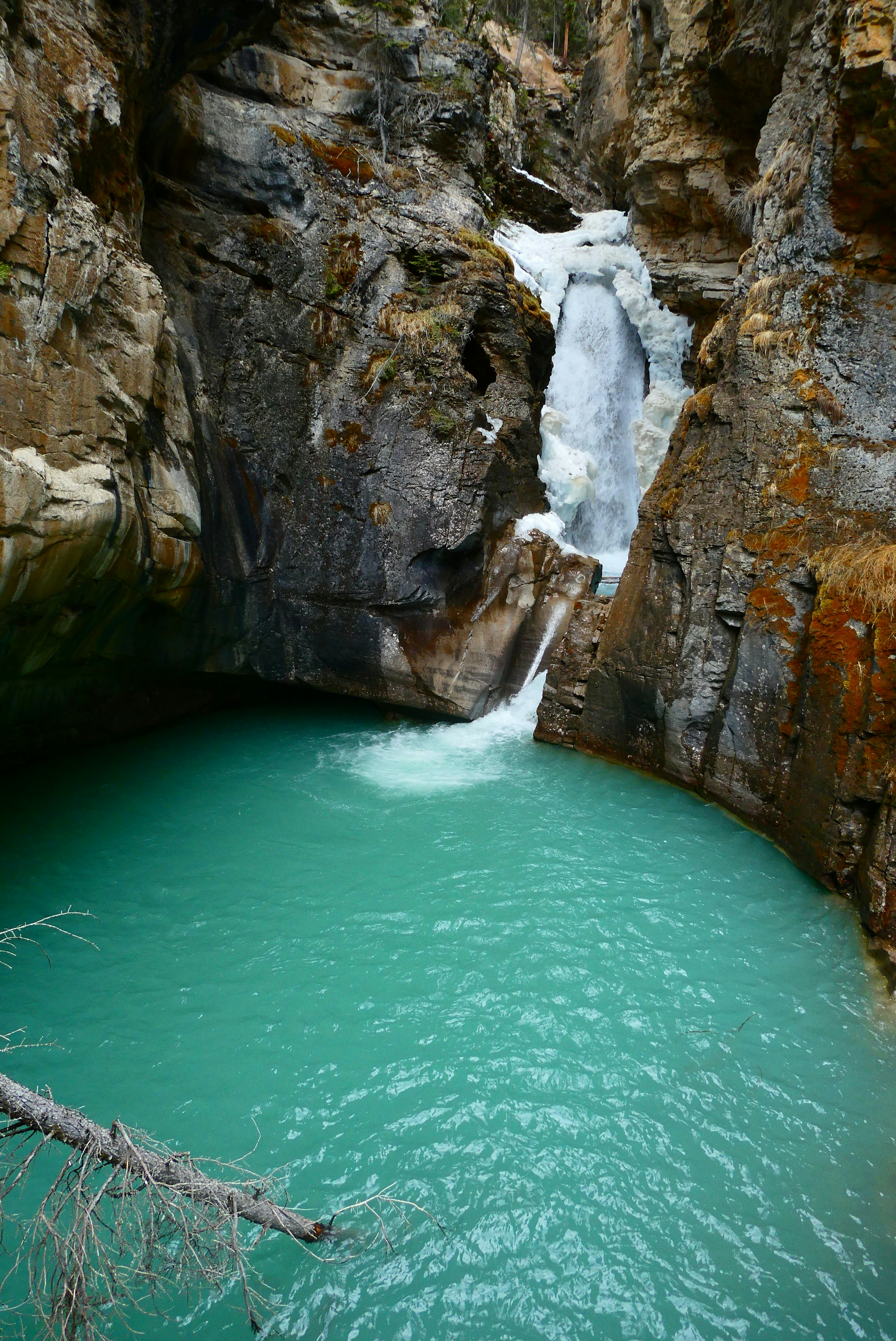 A waterfall cascades down rocky cliffs into a turquoise pool, surrounded by rugged stone formations and sparse vegetation.