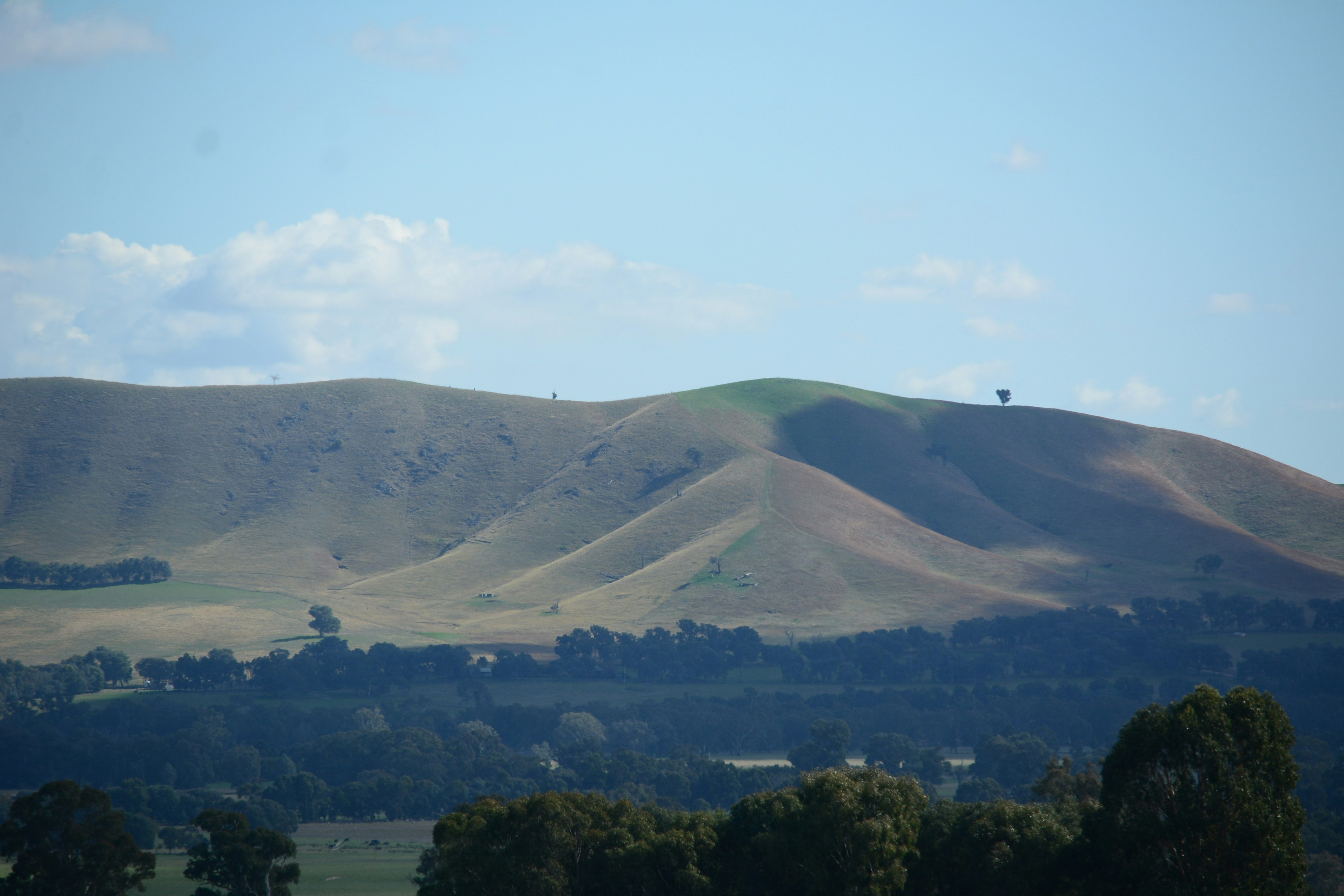 Gentle rolling hills under a clear blue sky with scattered clouds.
