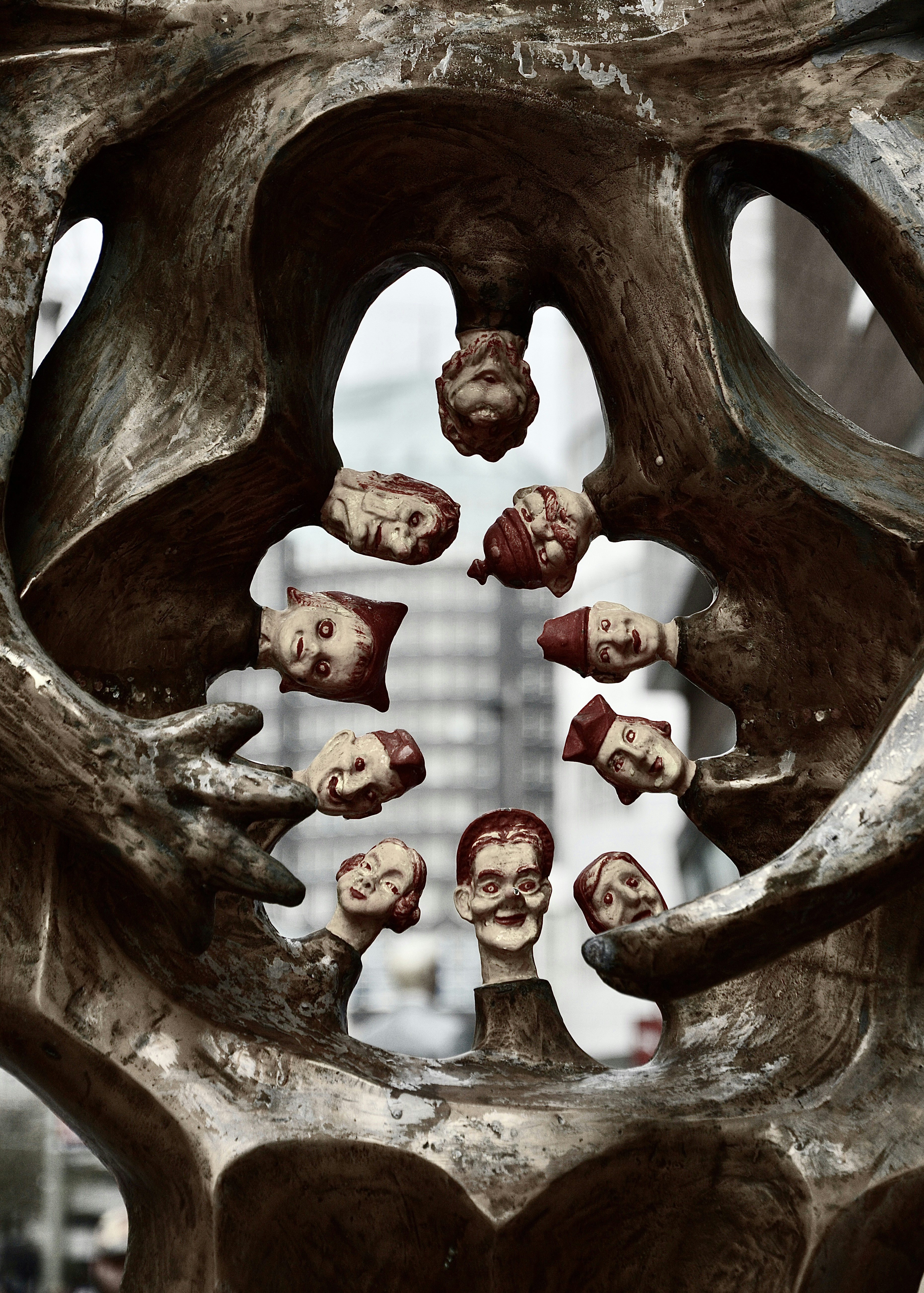 Intricate sculpture featuring a collection of stylized human heads emerging from a textured frame, creating a surreal visual narrative.