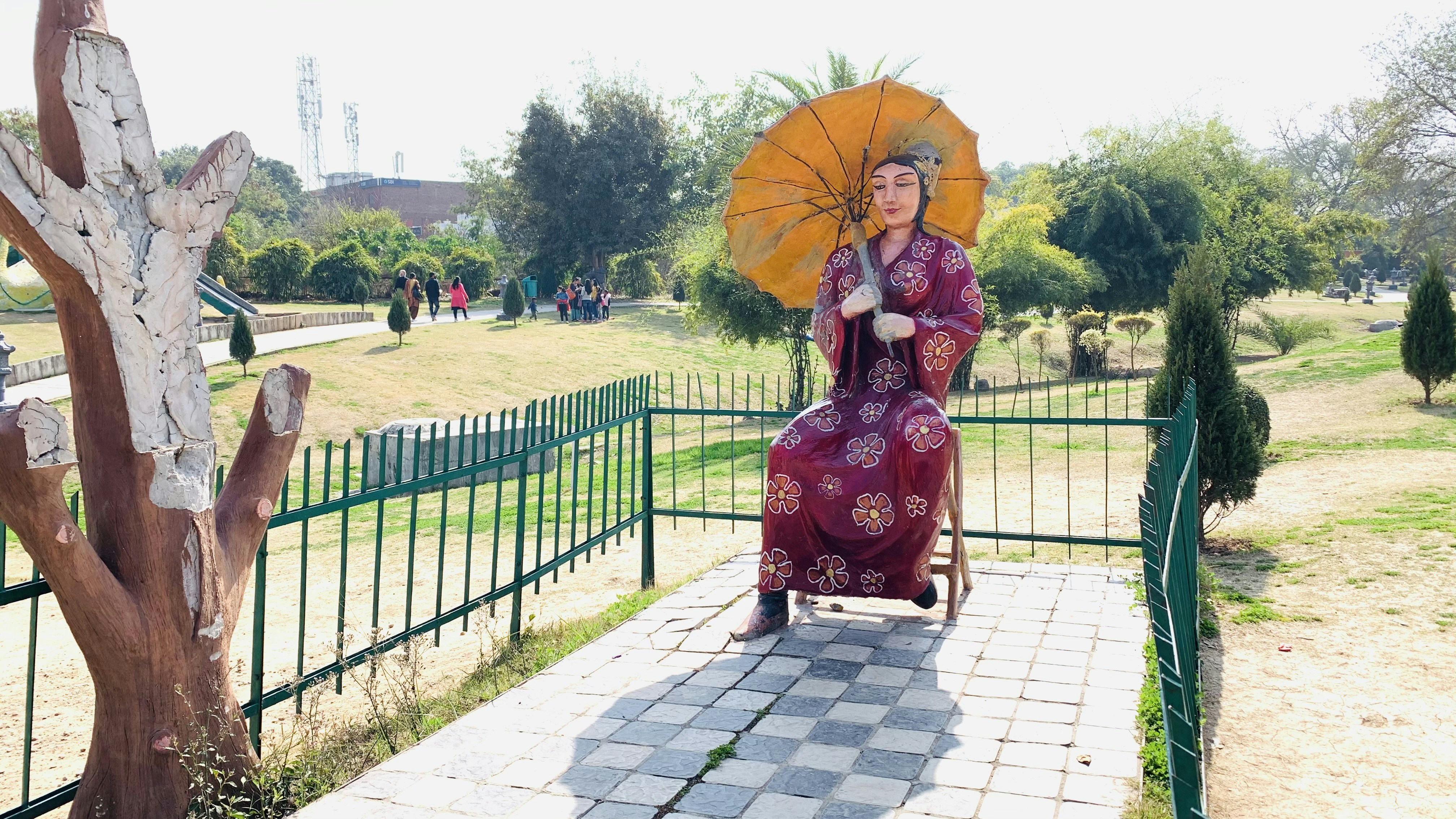 Woman in a patterned dress holding a yellow umbrella, walking on a garden pathway.