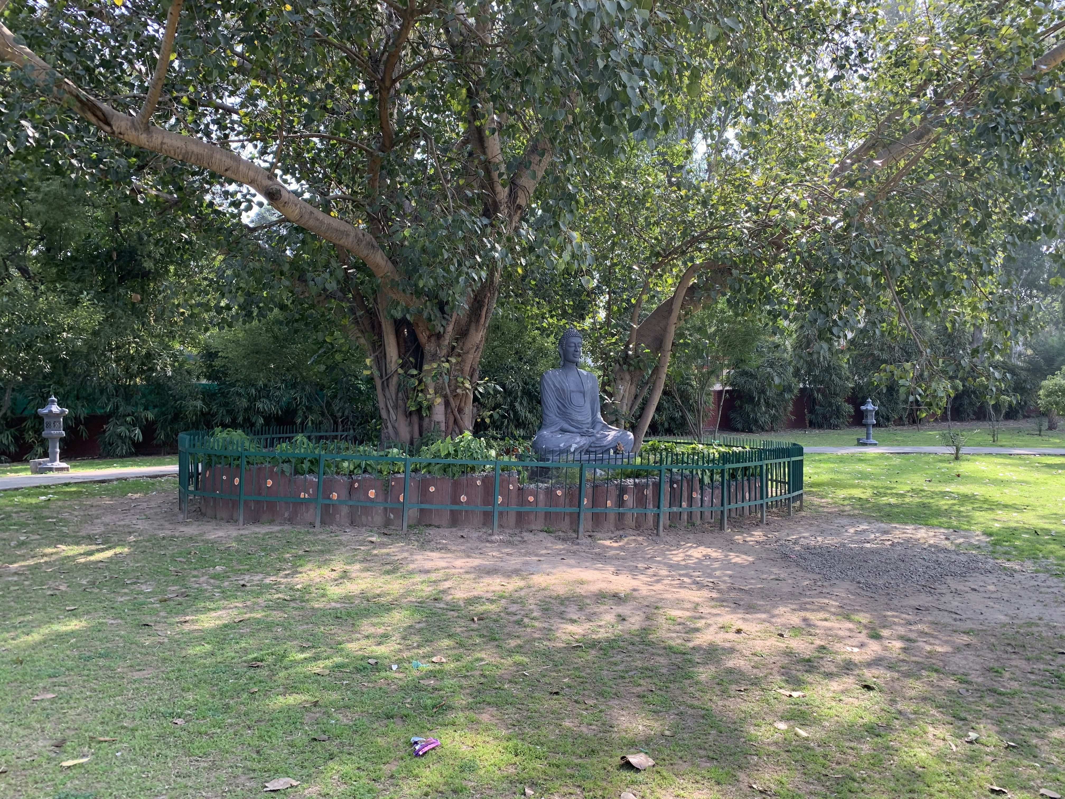 Circular Garden Centerpiece: A Meditative Statue Amid Dappled Park Shade