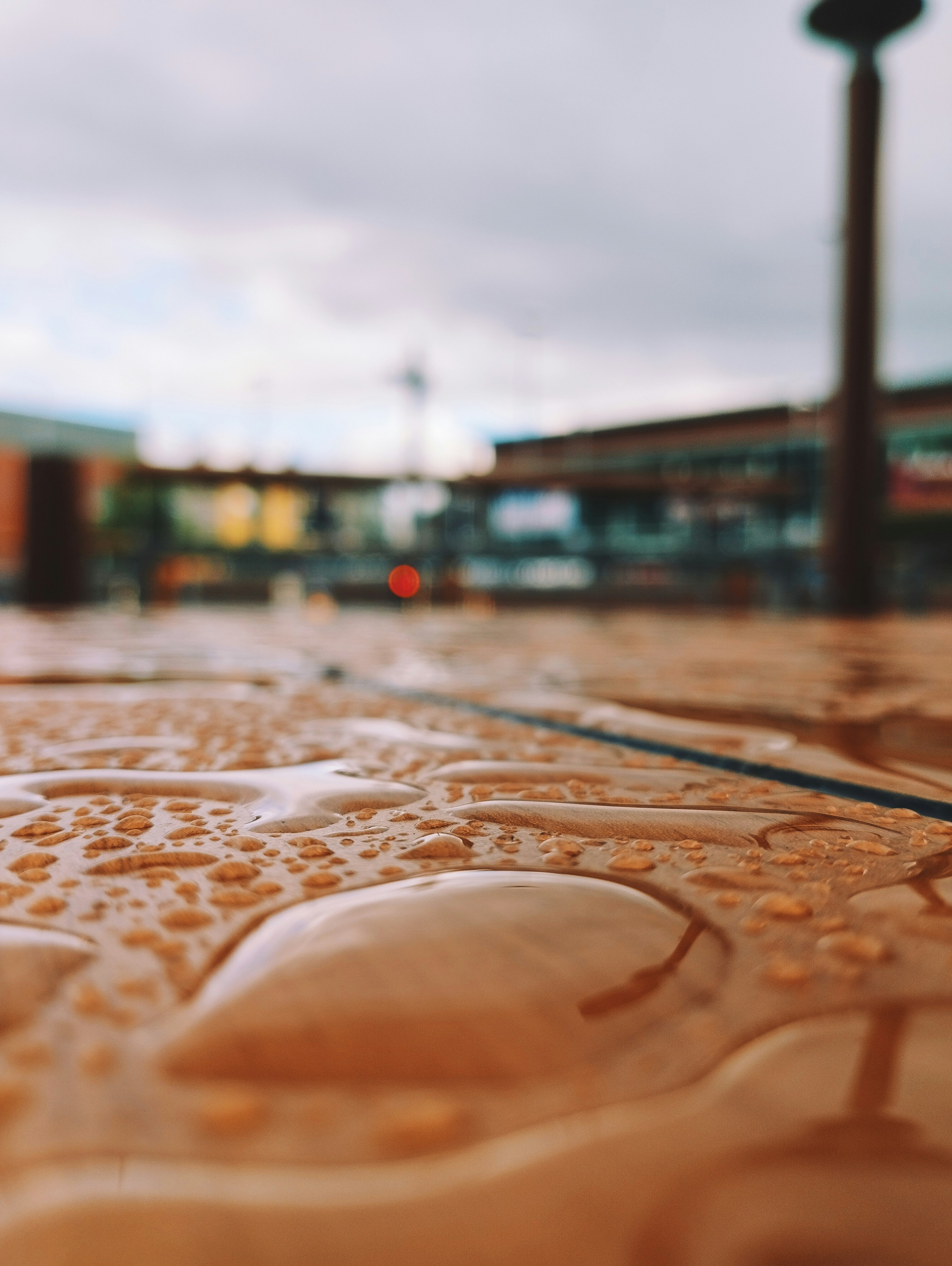 Close-up of wet, textured tiles with water droplets in the foreground and a blurred urban background, emphasizing reflective surfaces and shallow depth of field.
