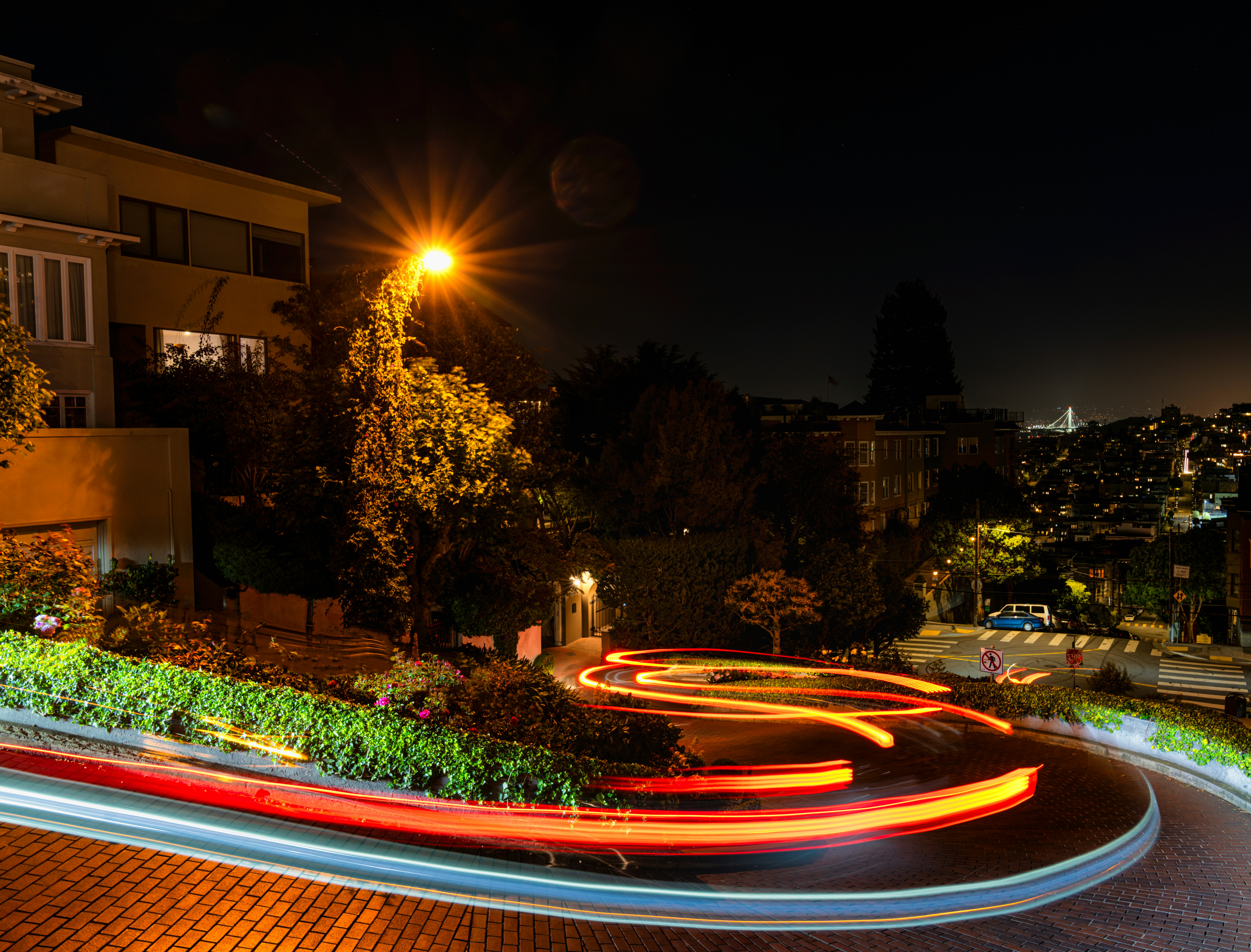 Long exposure of car taillights winding down a steep, narrow street at night.