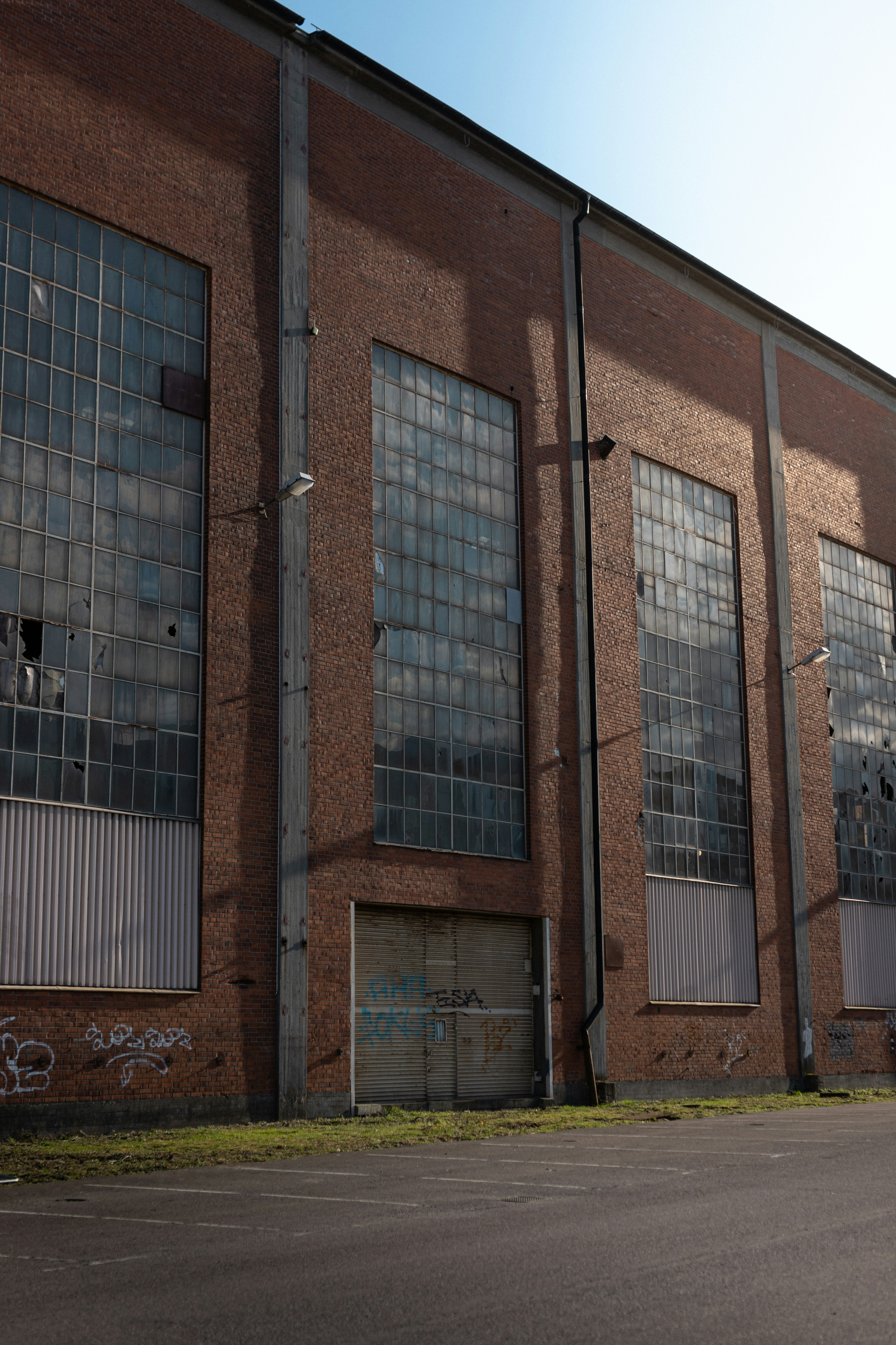 Abandoned industrial building with large, broken windows and graffiti on the brick walls. The scene captures the passage of time and urban decay.
