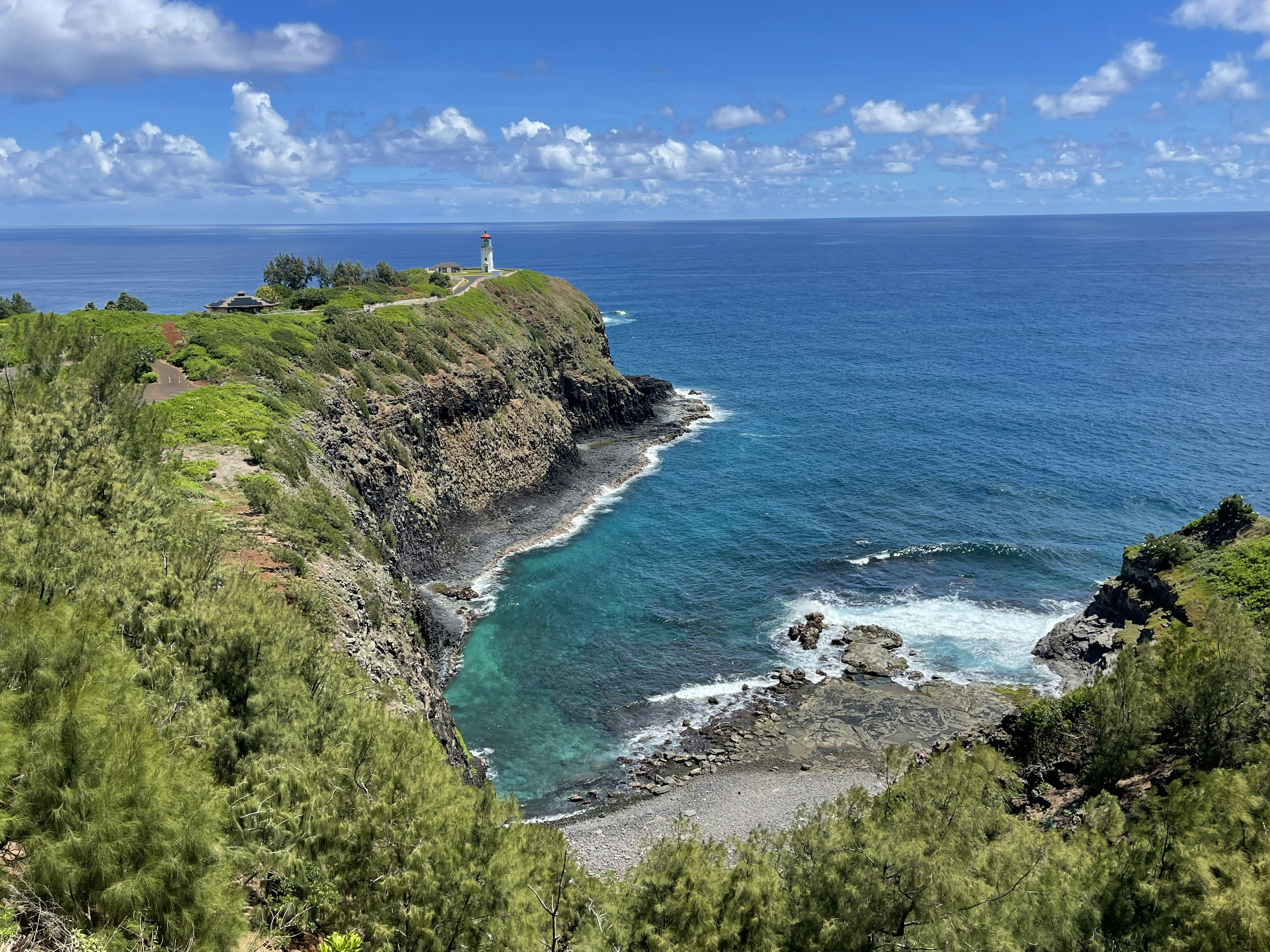 Lush green cliffs meet the vibrant blue ocean, with a lighthouse standing sentinel at the edge. Gentle waves lap against the rocky shoreline.
