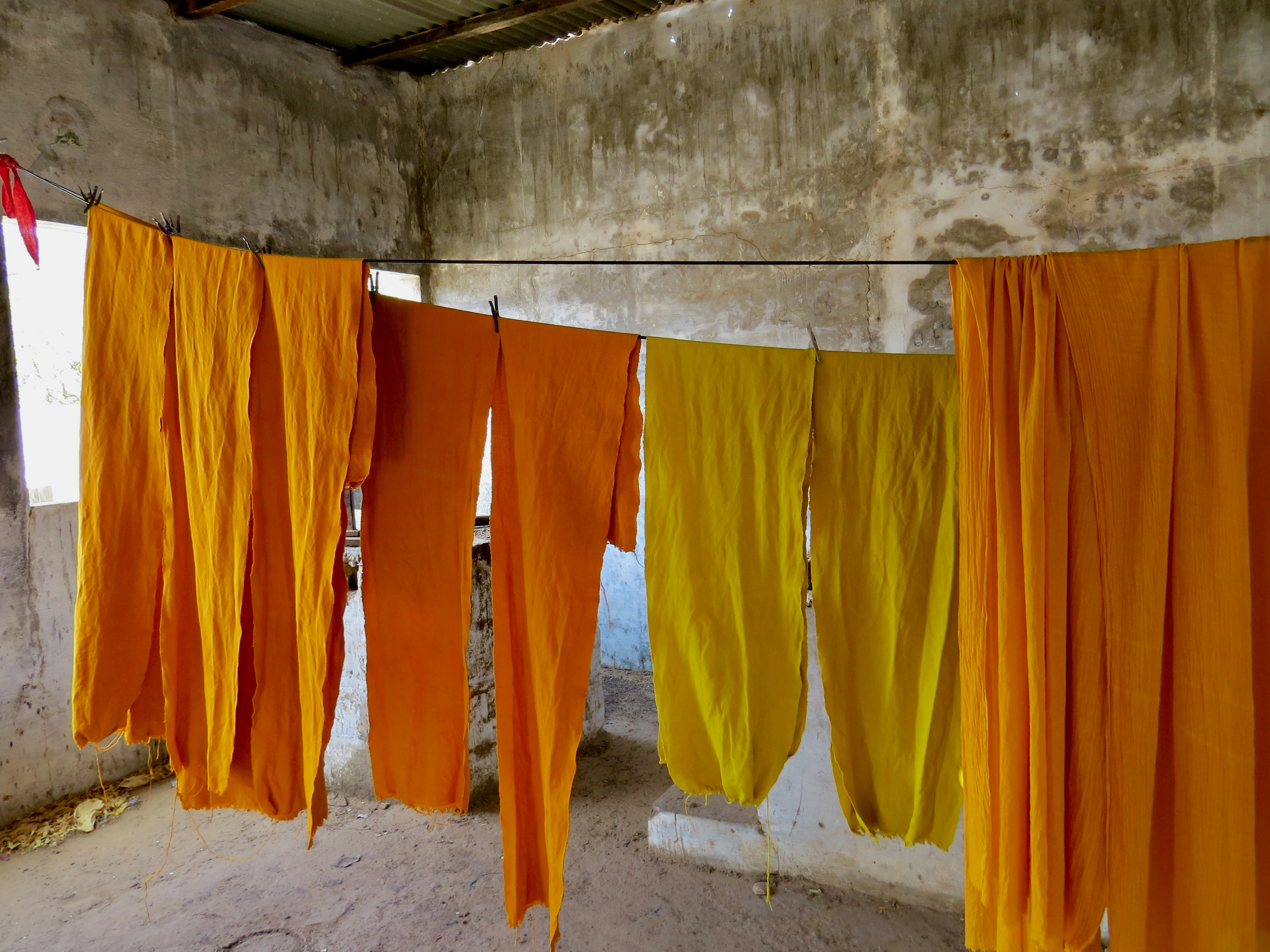 Bright orange and yellow fabrics hanging on a line in a weathered interior, showcasing traditional textile drying techniques.