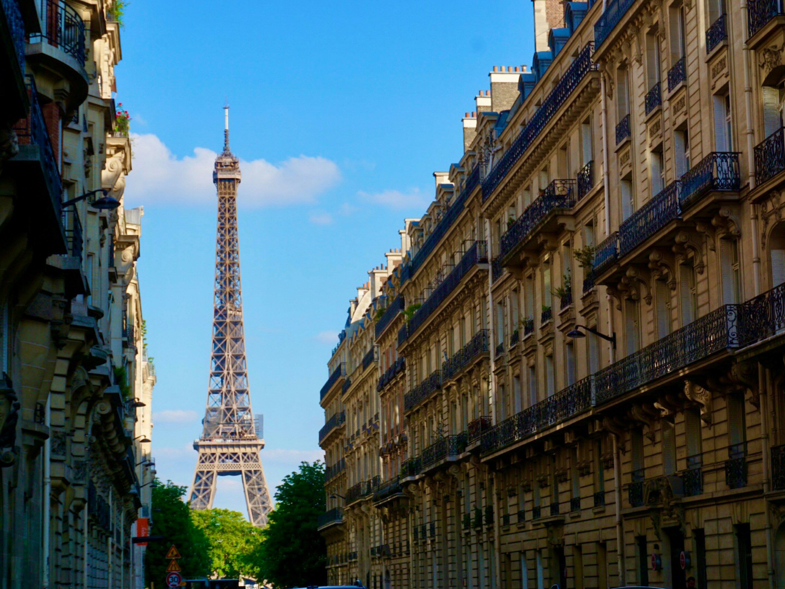 Eiffel Tower rising majestically at the end of a Parisian street, flanked by elegant buildings under a clear blue sky.