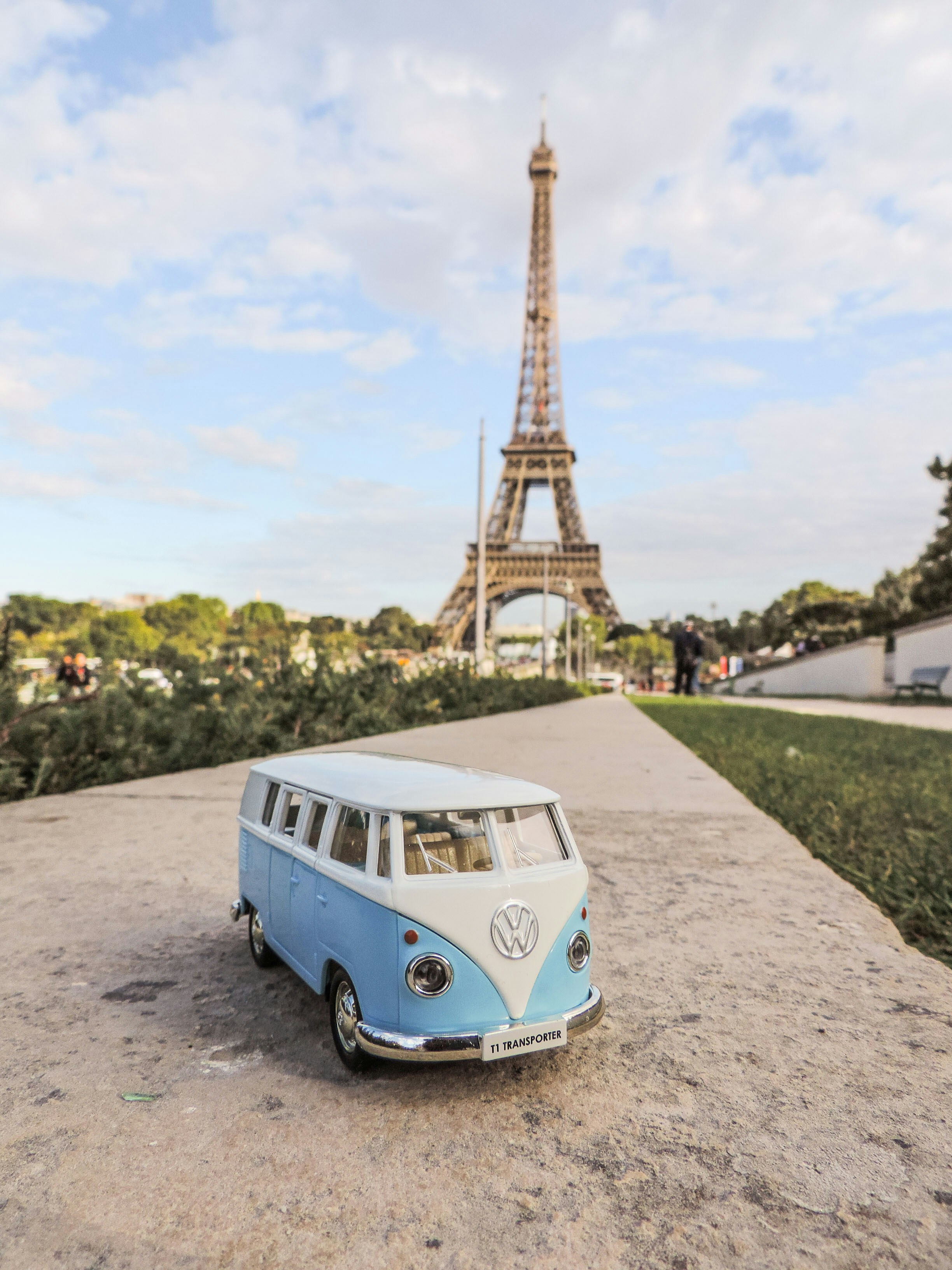 Photo of blue toy Volkswagen T1 at Eiffel Tower at background. Sunny day outside.