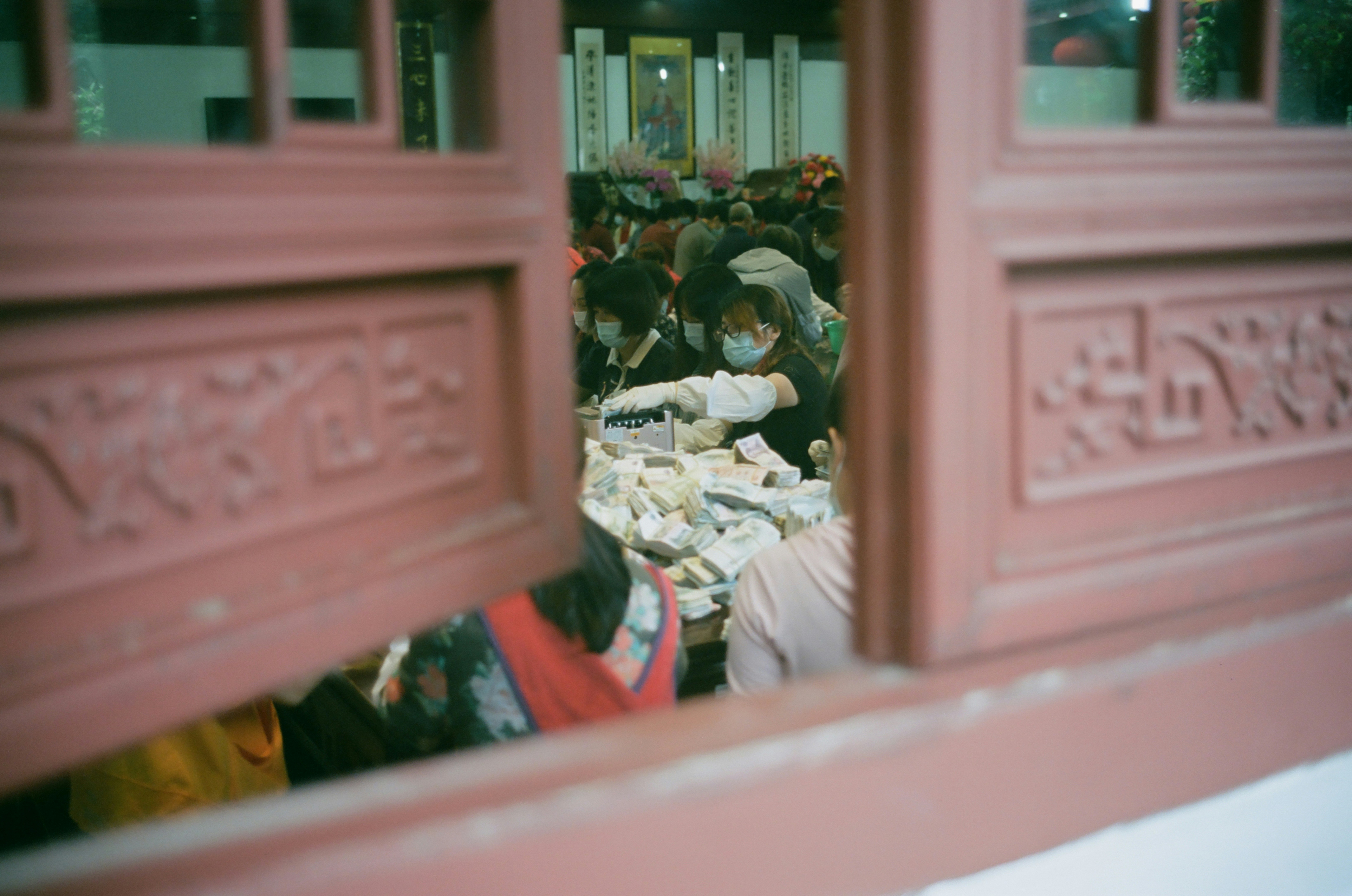 Gathering of people engaged in a traditional event, viewed through intricately carved window frames. The scene captures a moment of cultural significance and community interaction.