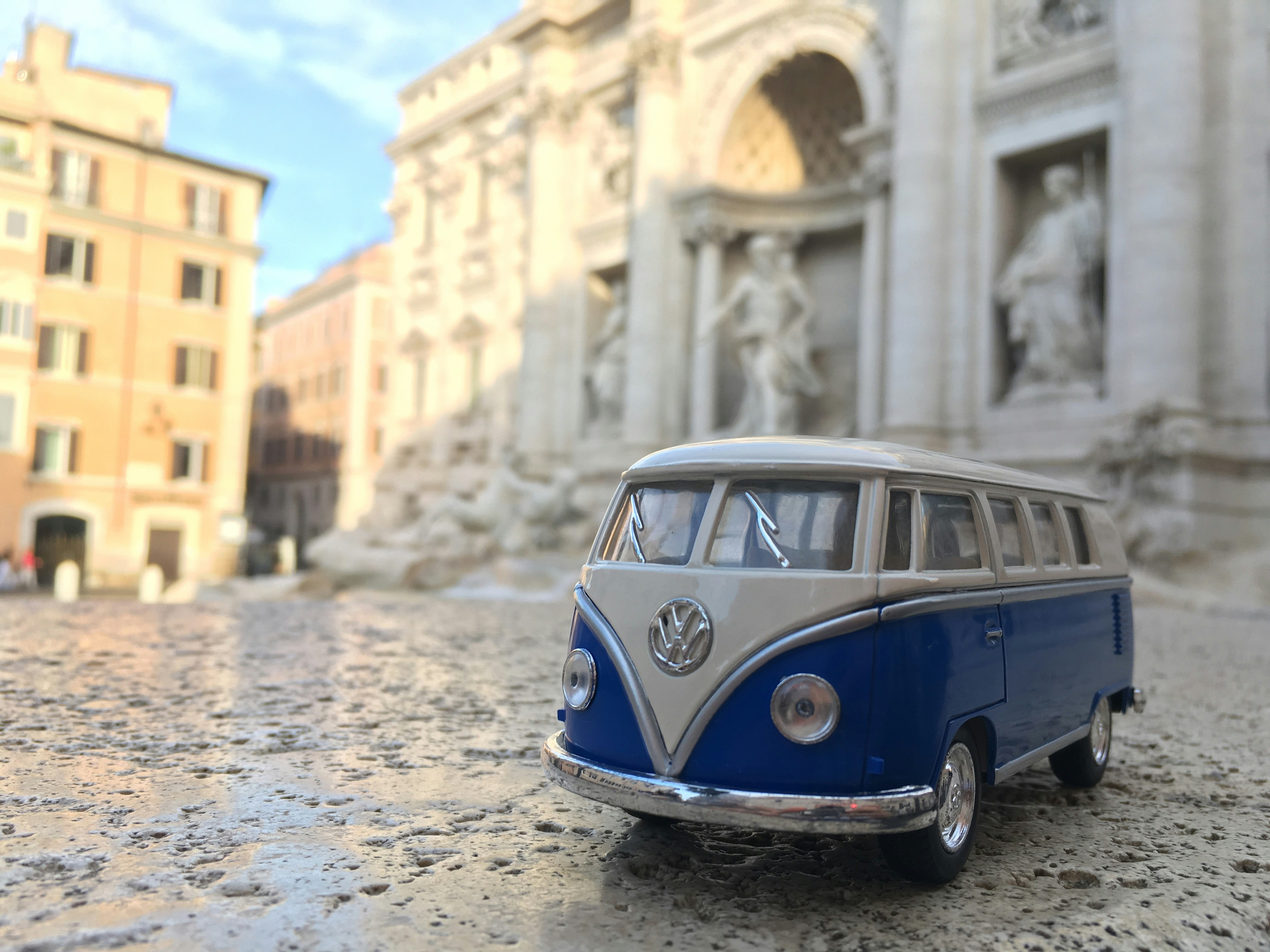 Model blue Volkswagen van placed on cobblestones in front of a grand historic building.