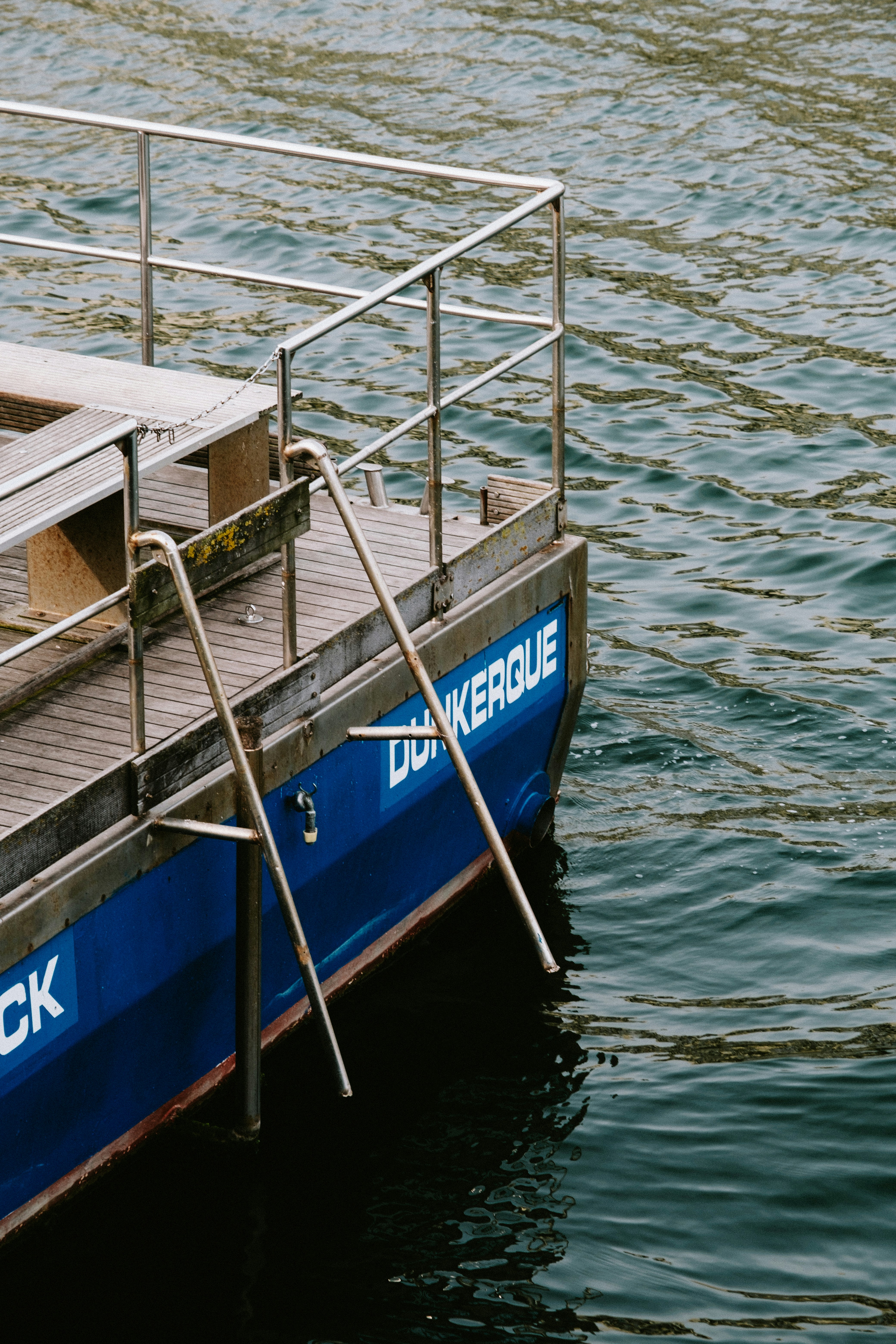 Dunkerque Pier Edge: Steel Rails Framing a Blue Hull by Quiet Water