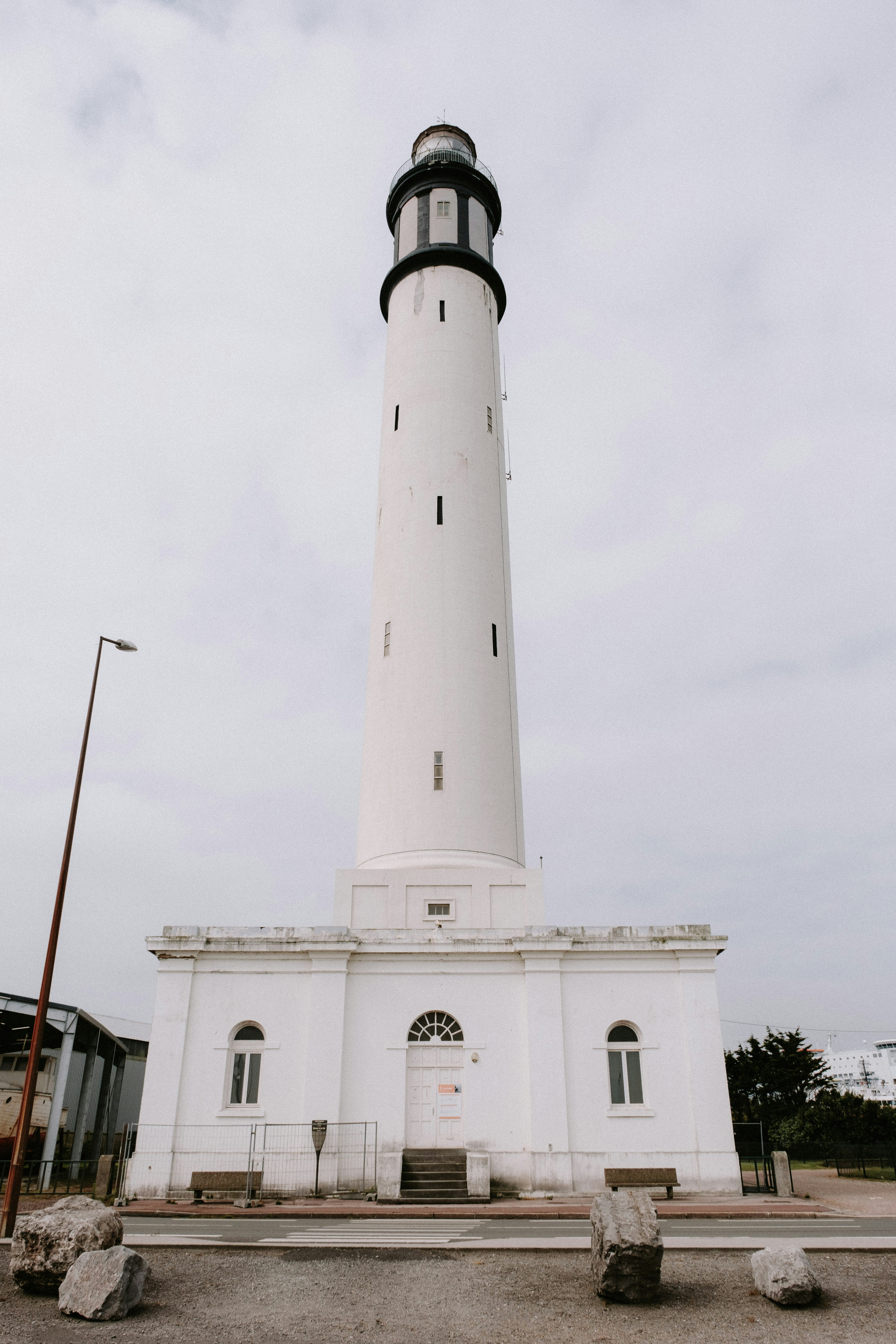 A tall white lighthouse stands prominently against a cloudy sky, showcasing its architectural details and historical significance.
