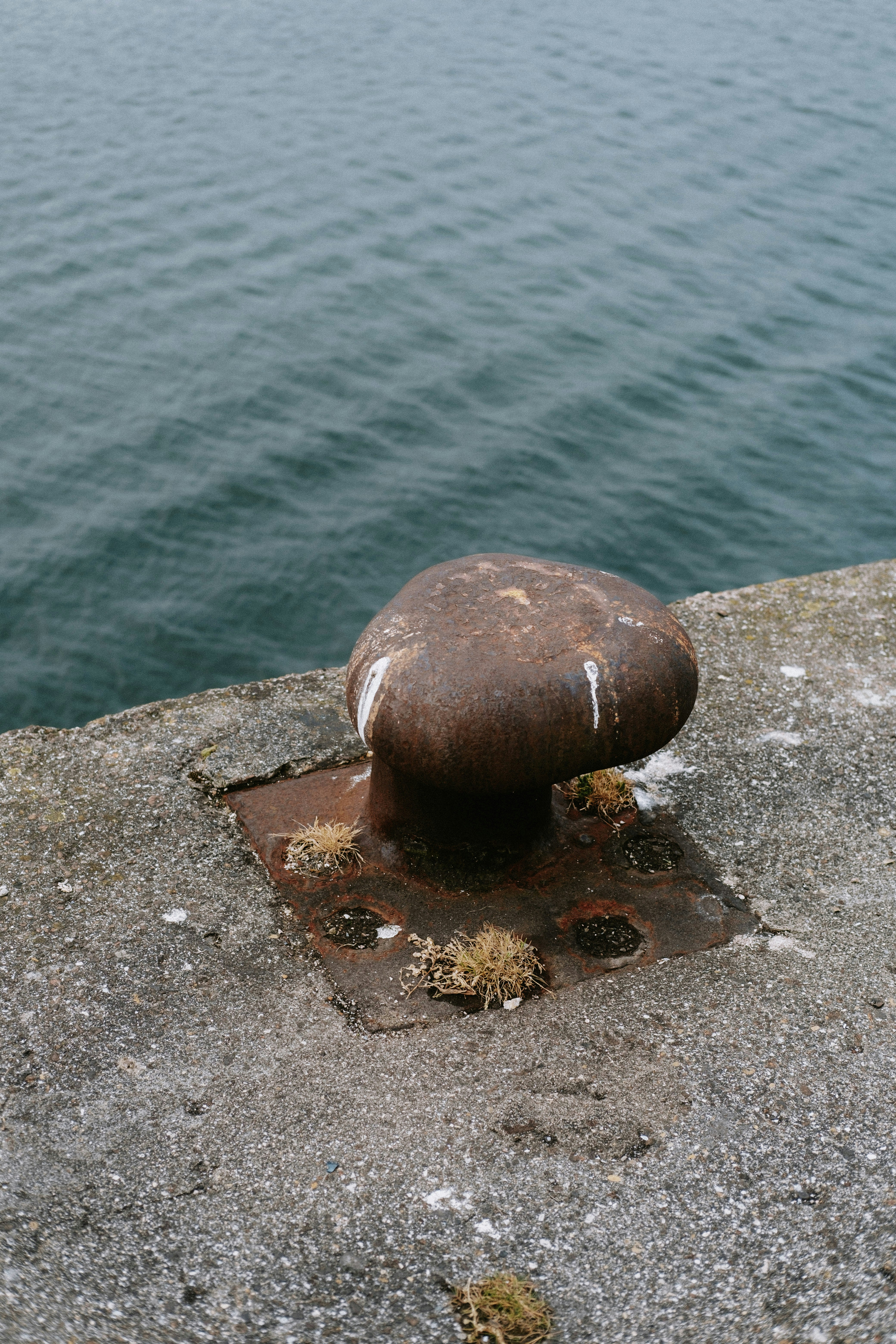 Rust-Patina Bollard on a Weathered Pier Over Quiet Teal Waters