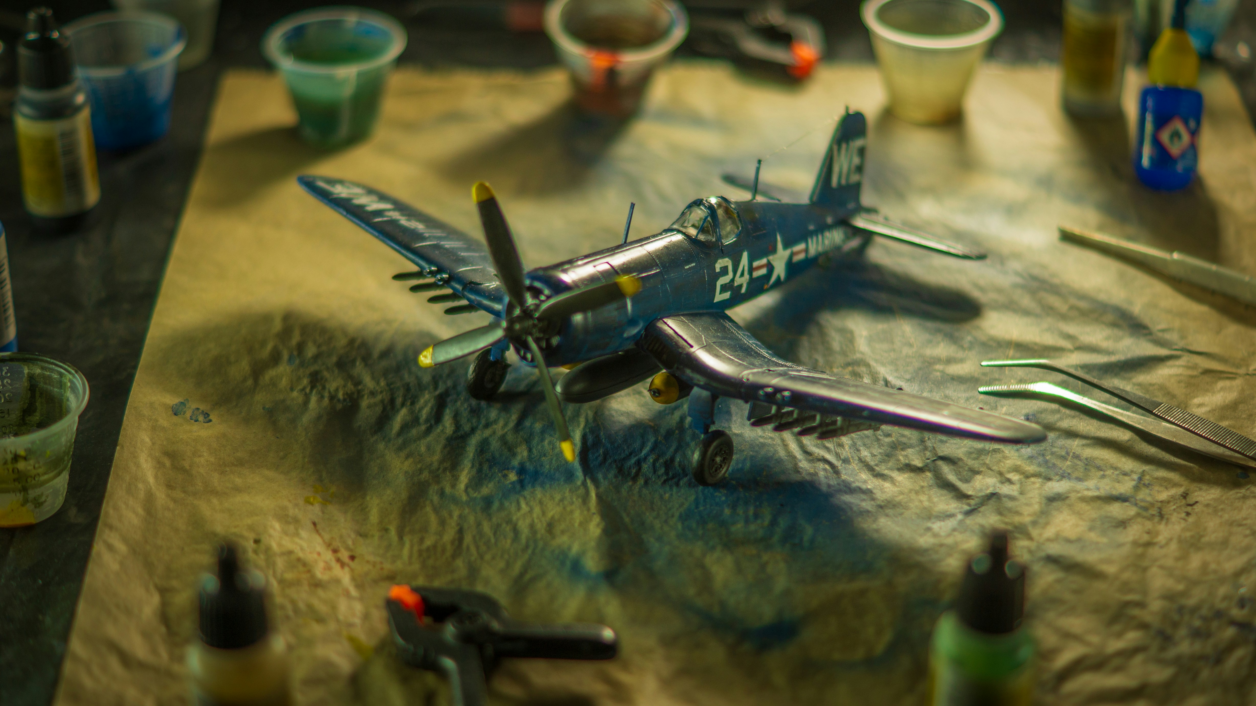 Detailed model airplane surrounded by various paint containers and tools on a textured surface.