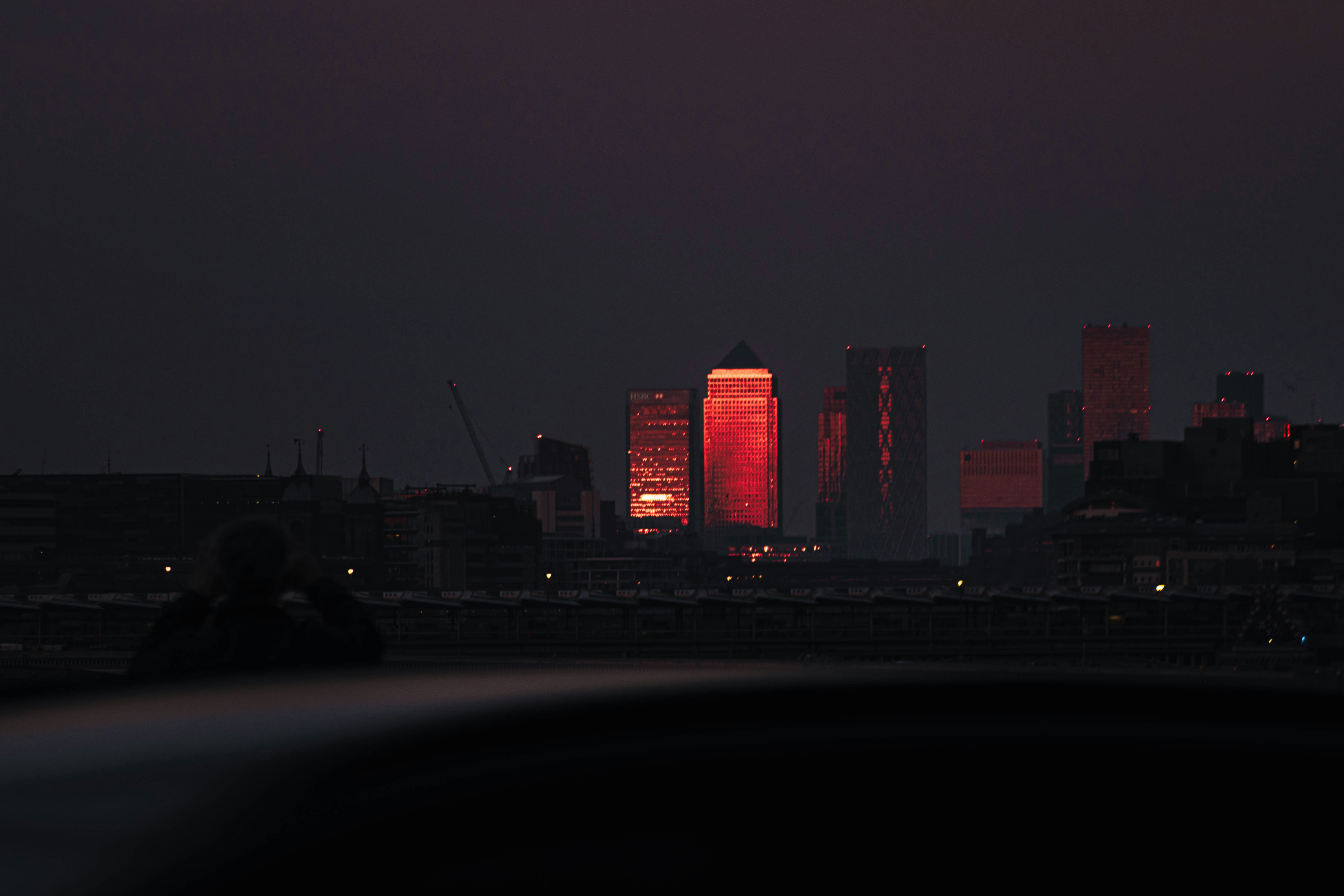 City skyline illuminated by the warm glow of sunset, with silhouetted buildings against a dusky sky.