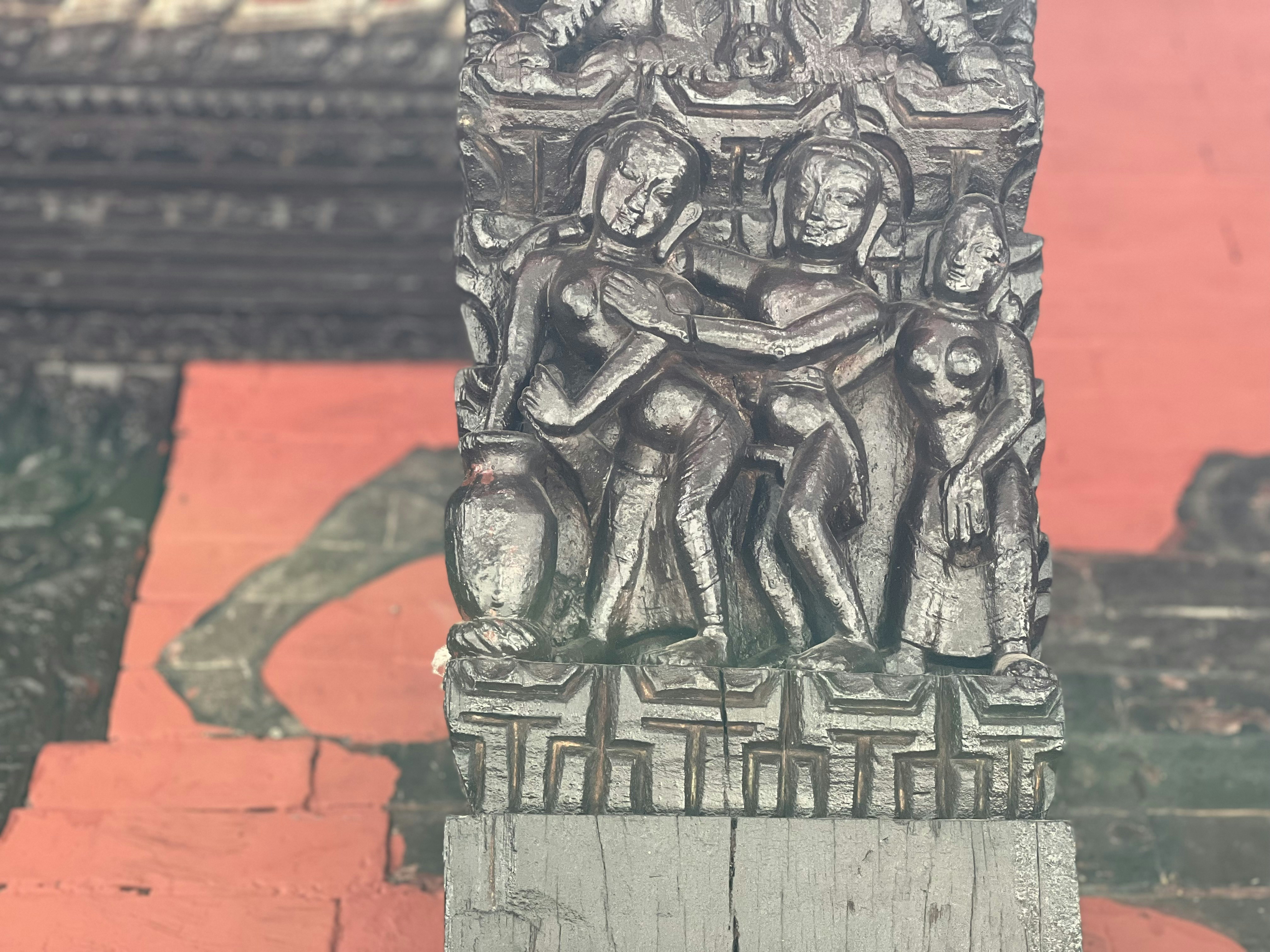 Intricate wooden carving depicting two figures in an intimate embrace, surrounded by symbolic elements, showcasing traditional craftsmanship.