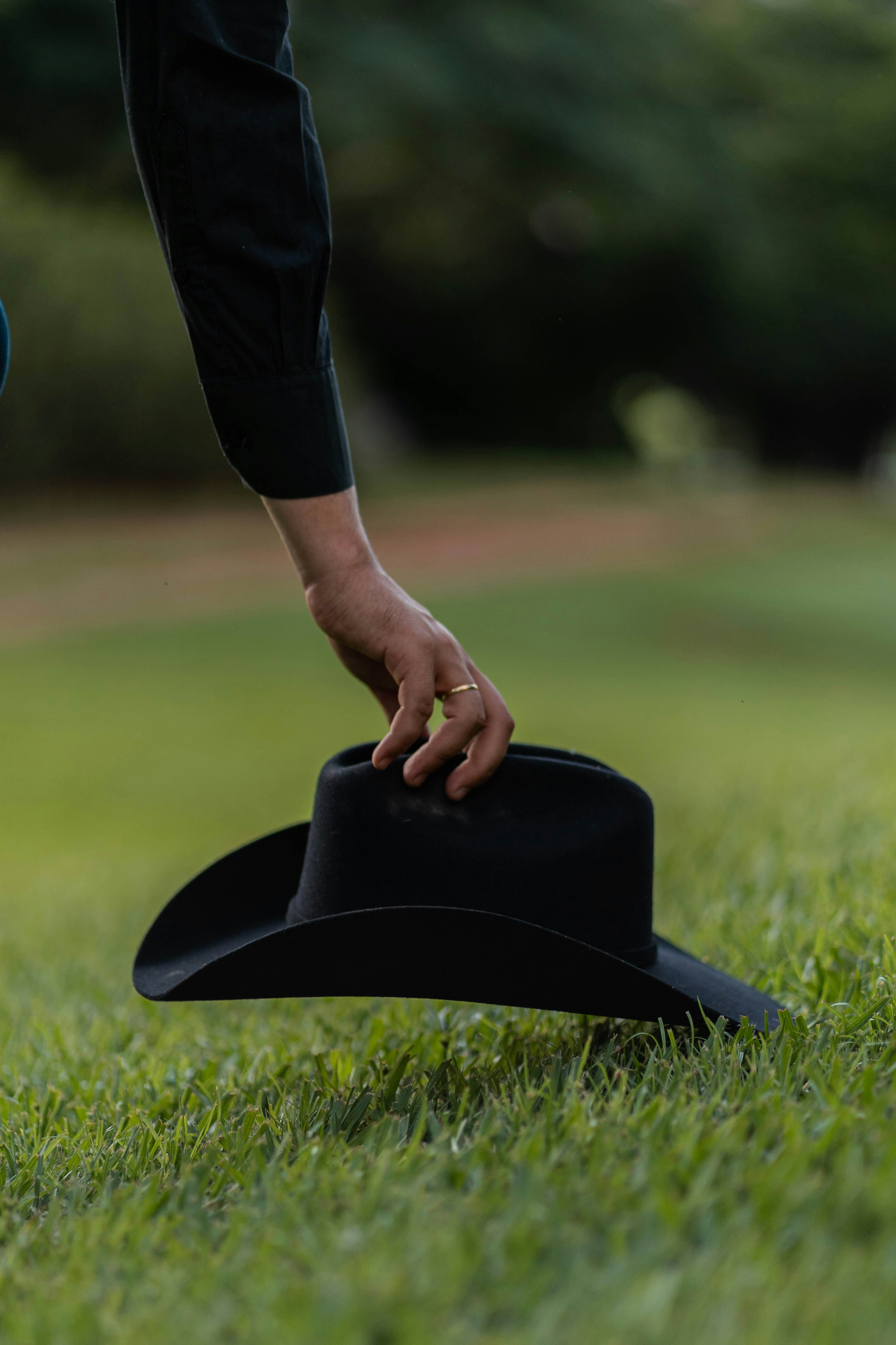 Quiet Gesture on the Grass: A Black Cowboy Hat in Focus