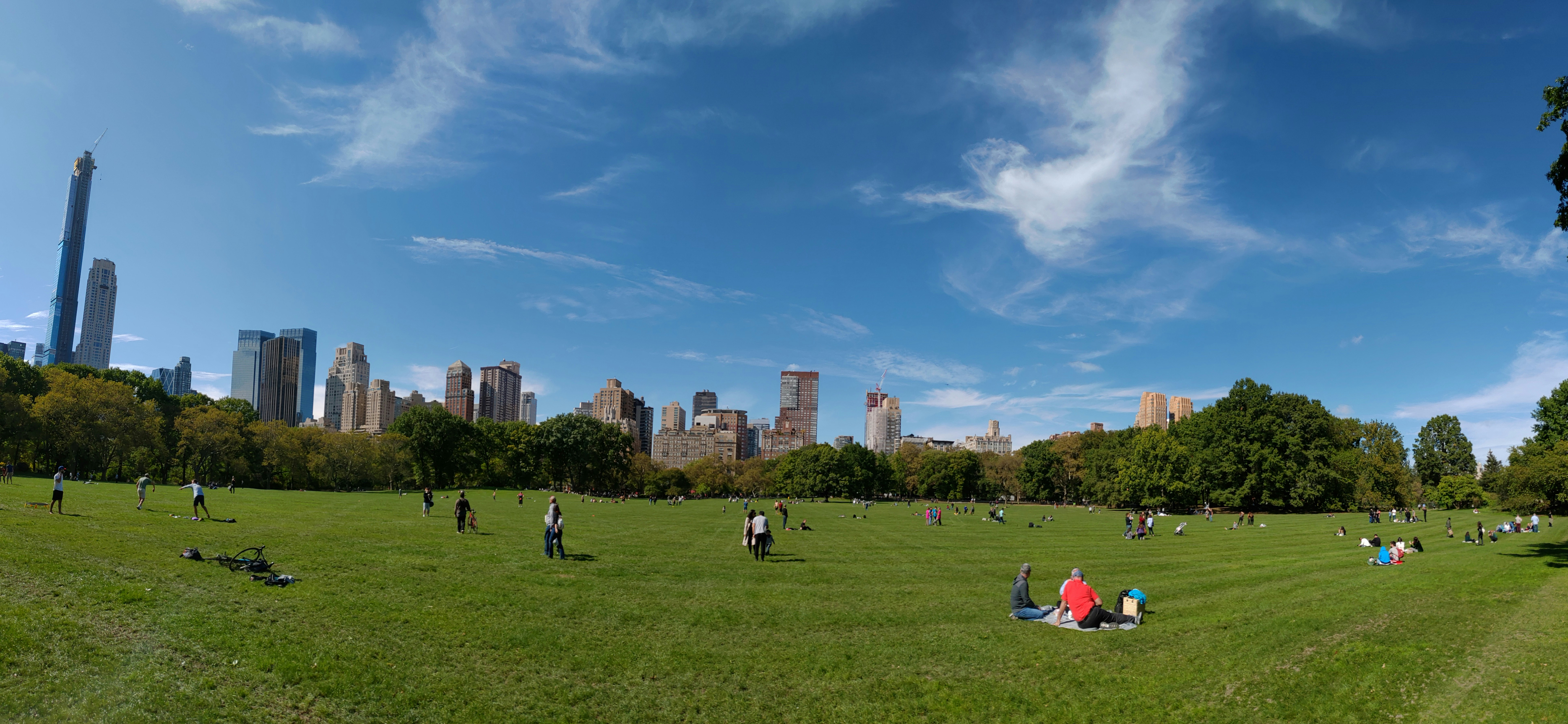 A group of people on a grassy field with buildings in the background ...