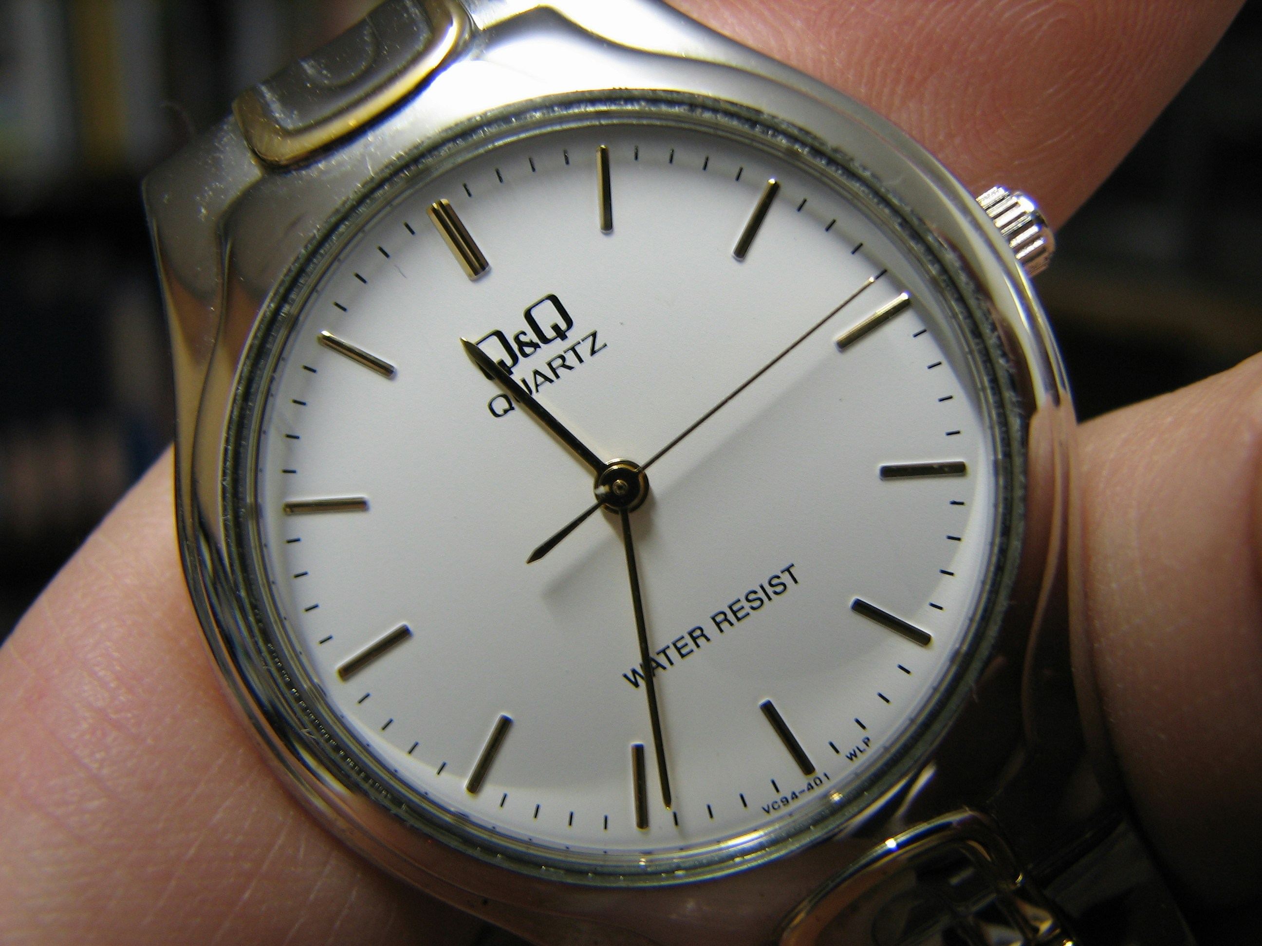 Close-up photograph of a stainless steel wristwatch dial with a white face, minimalist markers, and a slender second hand.