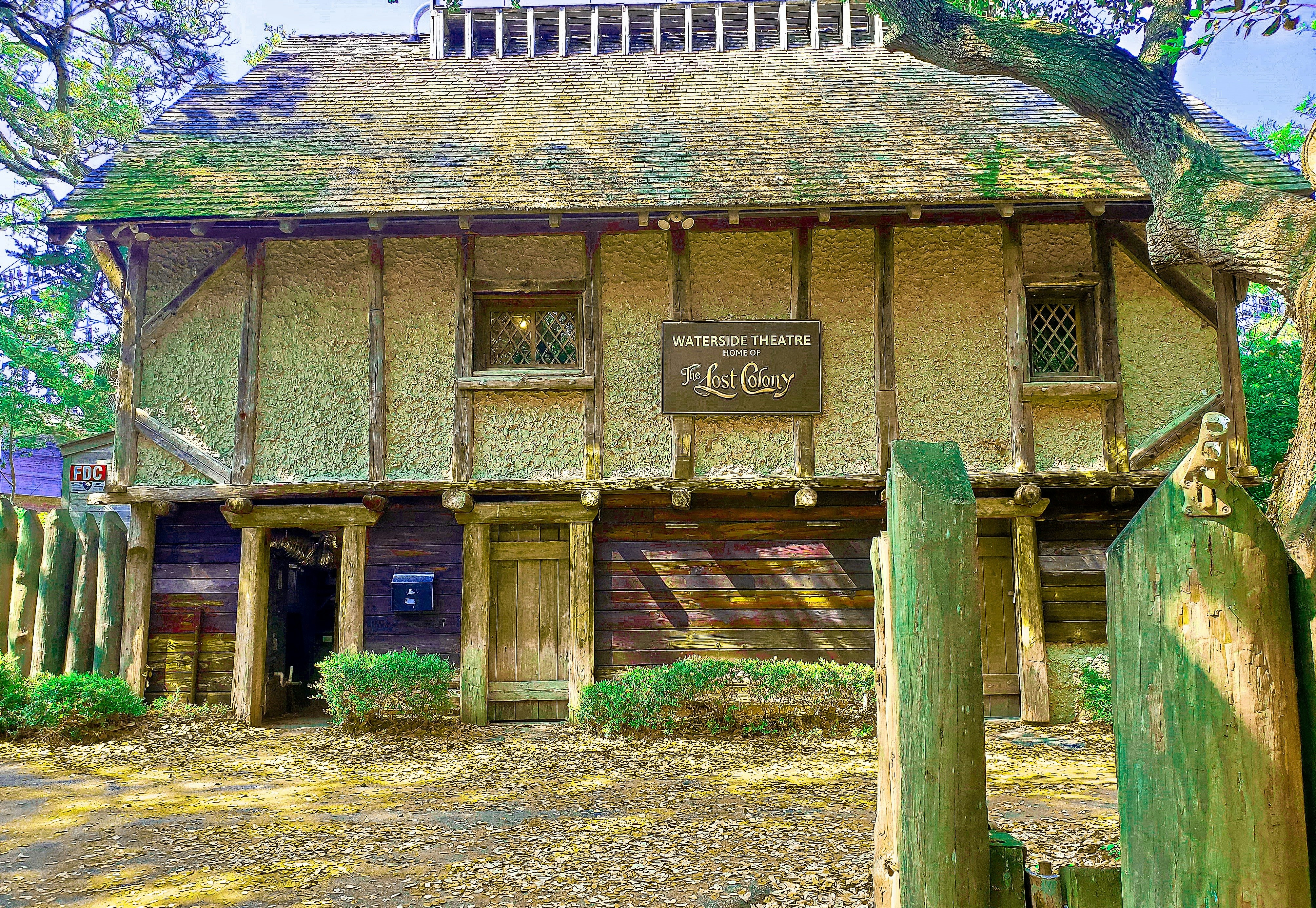 Historic wooden building with a thatched roof and a prominent sign under a canopy of trees.