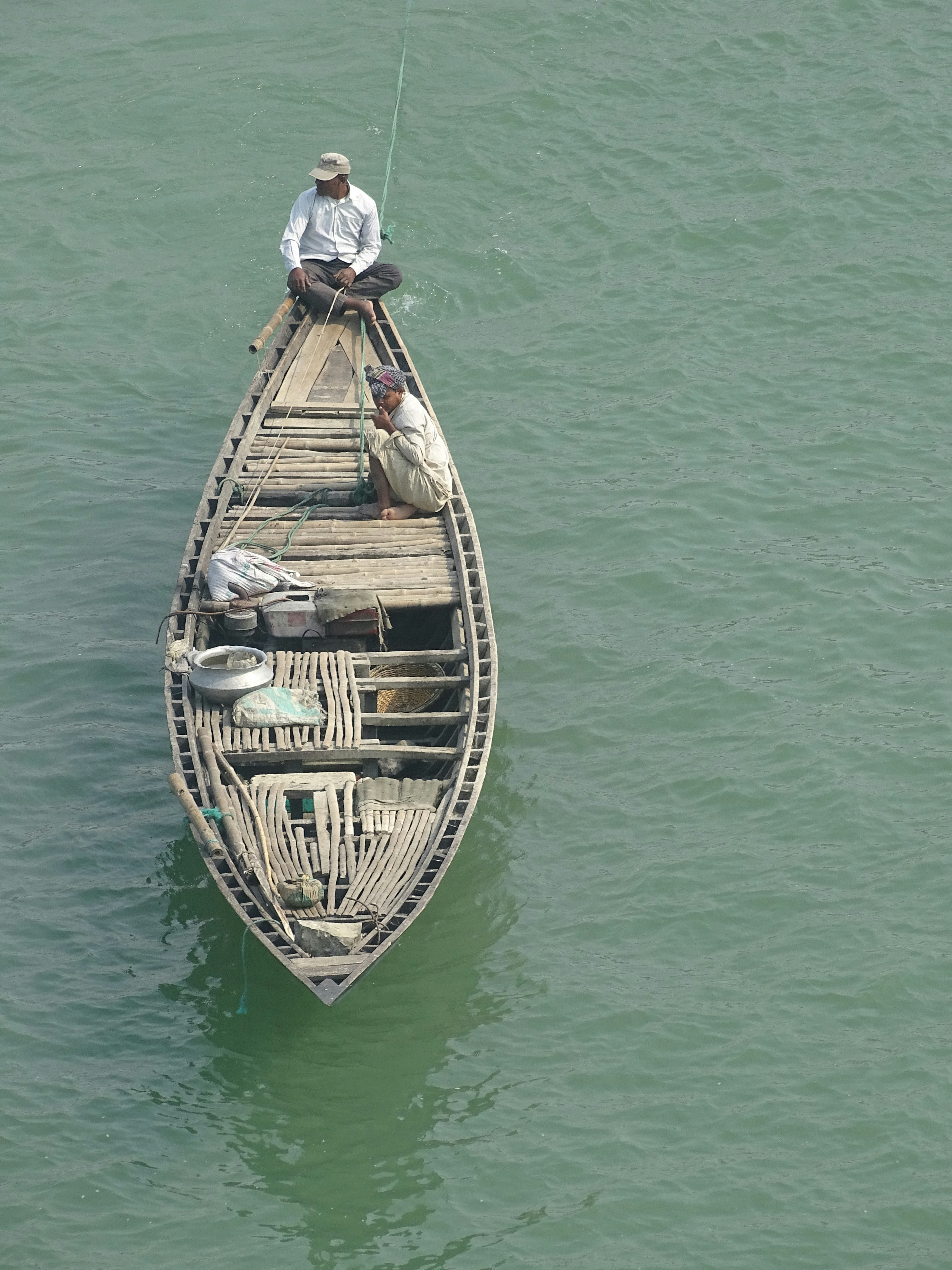 Wooden boat with two people drifting on calm green water.