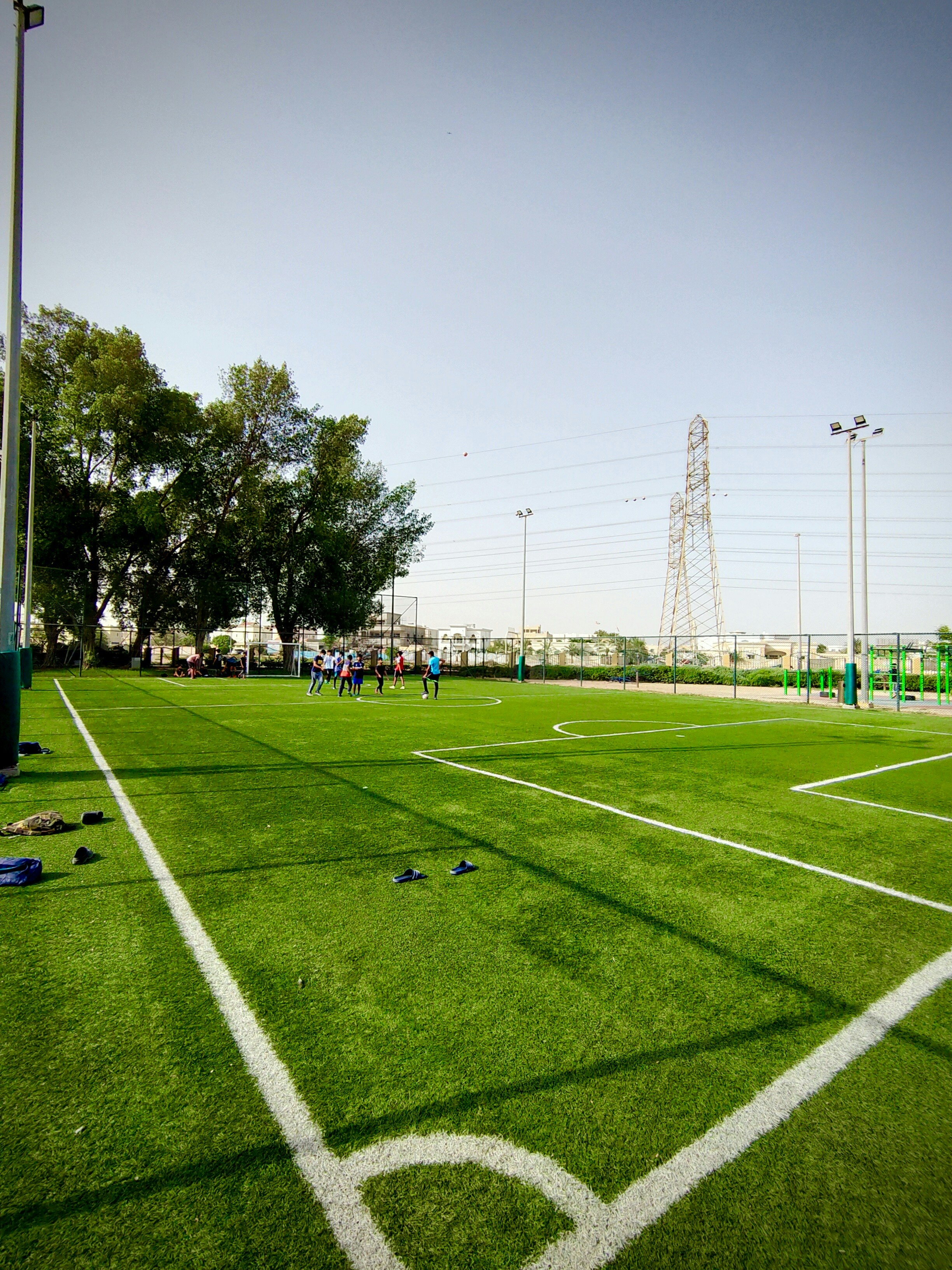 Youth soccer players engaged in a match on a vibrant artificial turf field, framed by lush trees and utility poles in the background.