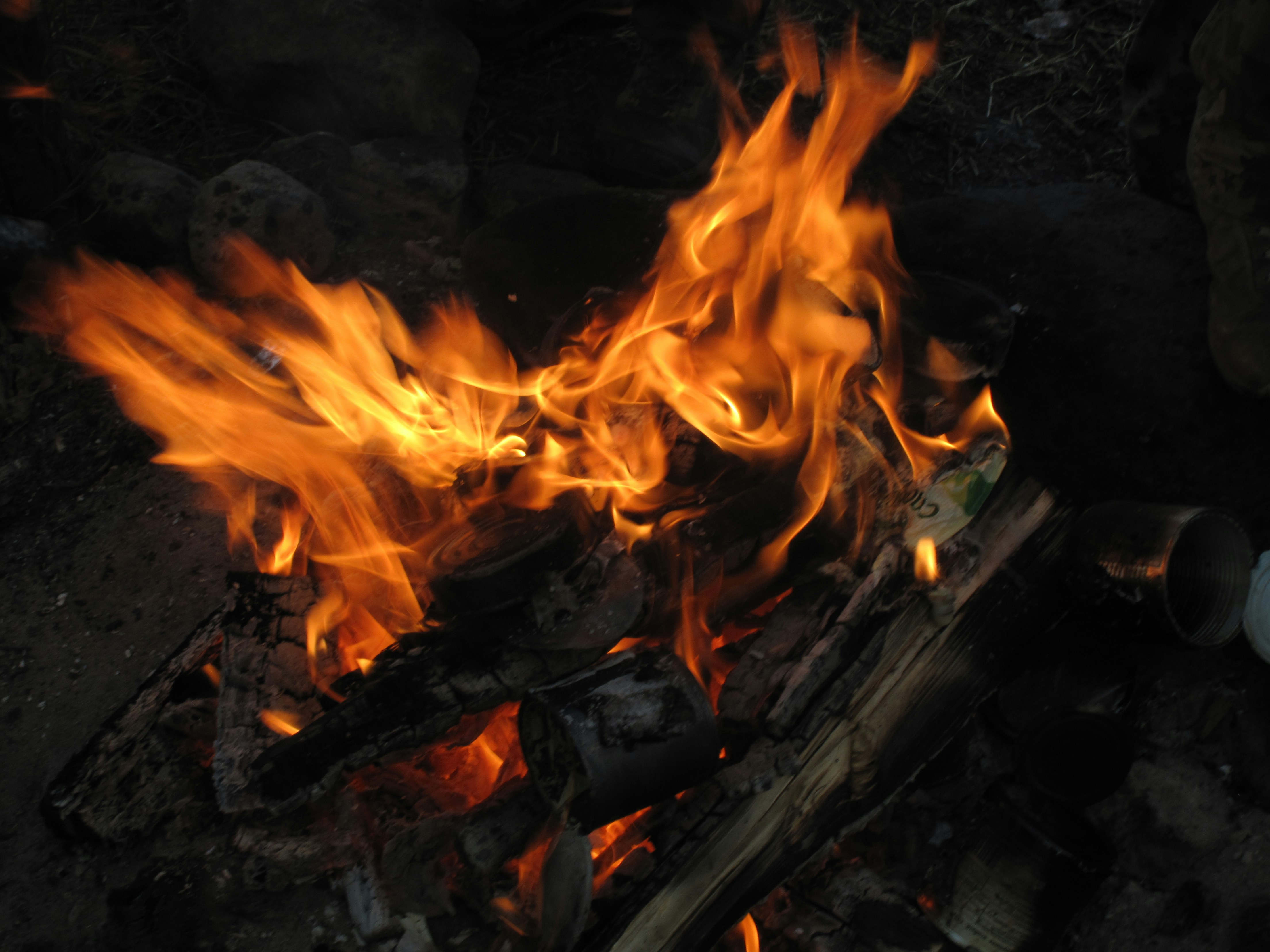 Flames dancing above a pile of logs and debris, creating a warm glow in the surrounding darkness.