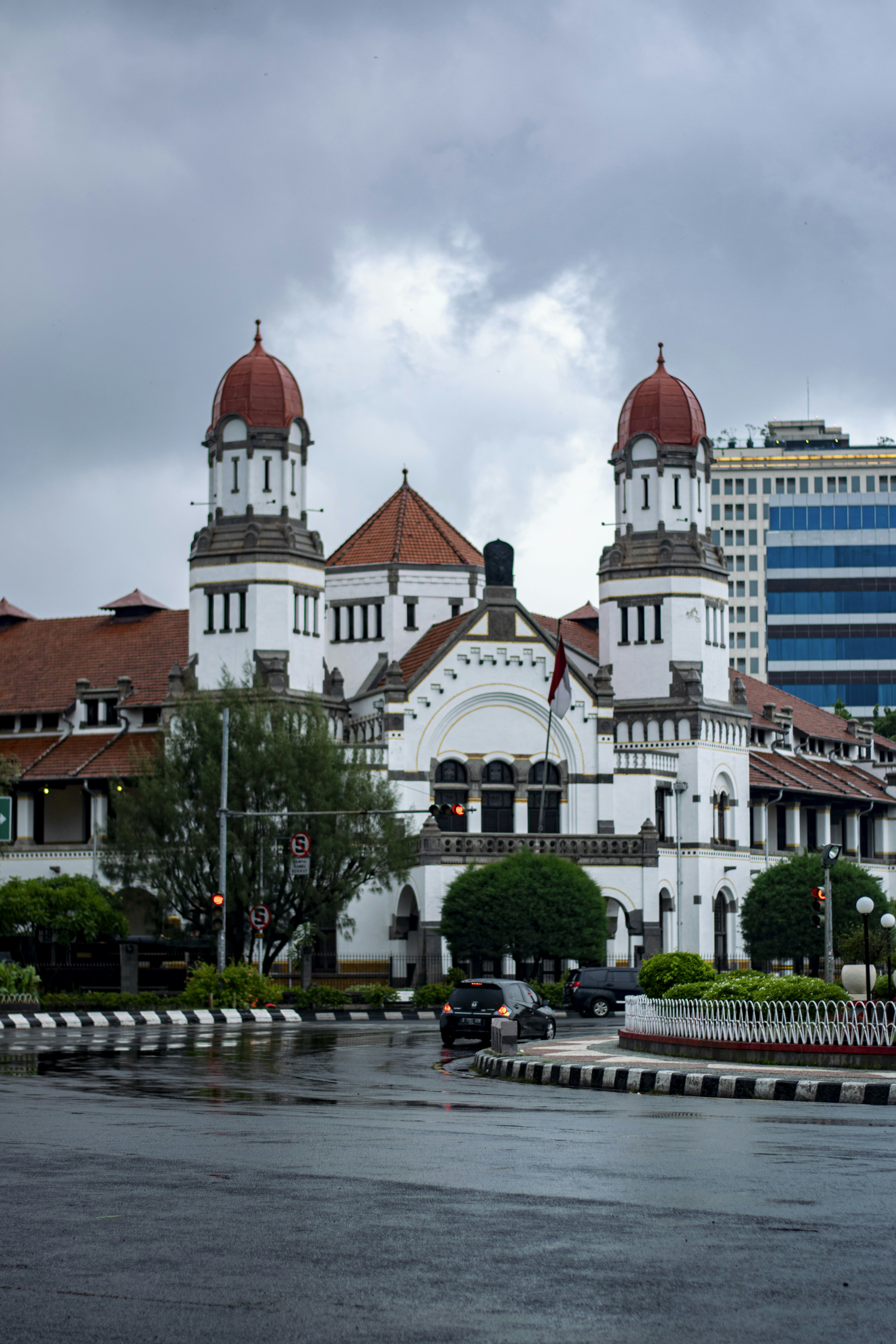 Historic building with distinctive domes and intricate architecture, surrounded by modern skyscrapers and lush greenery.