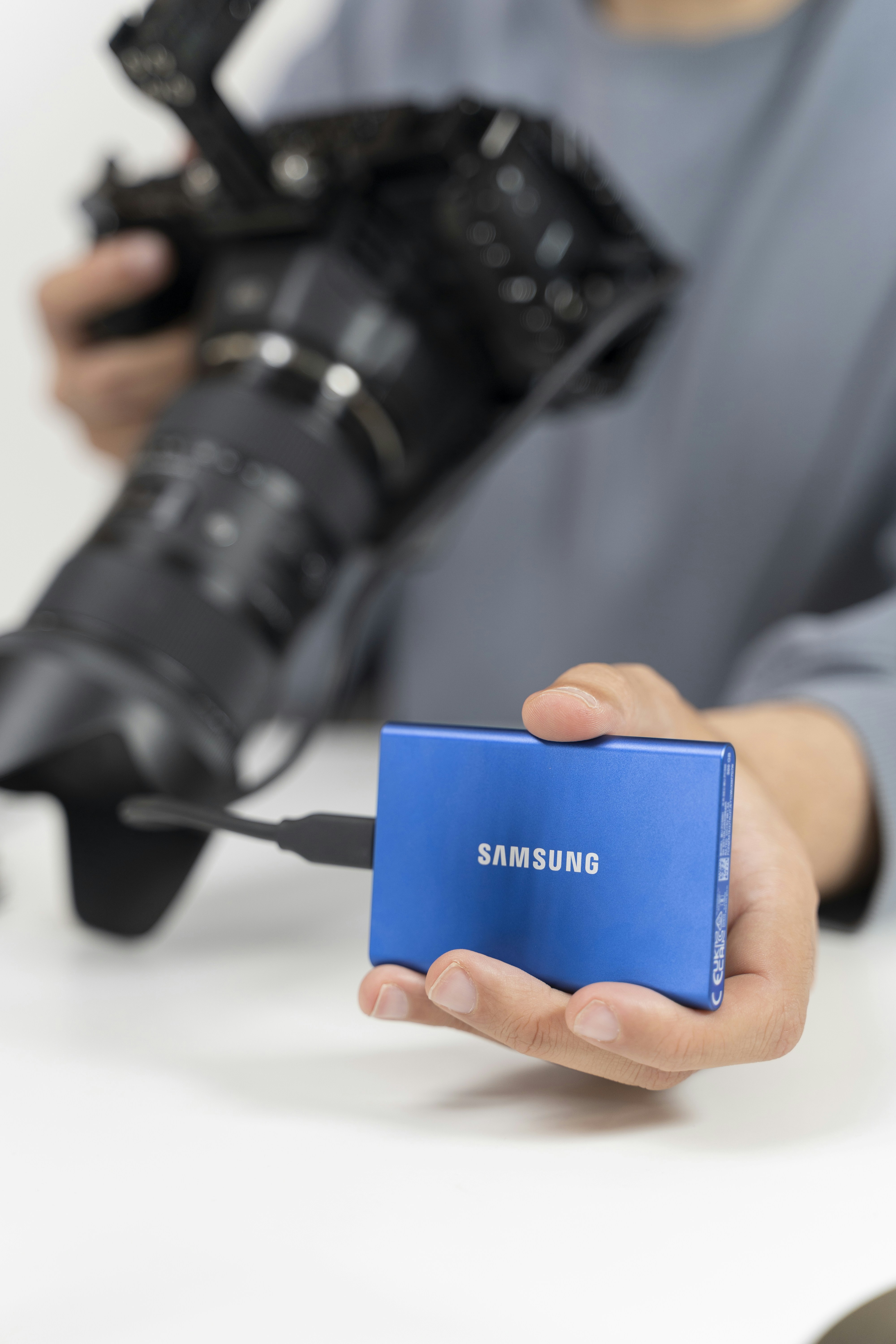 Blue Samsung SSD Gripped in Foreground, with a Cine Rig in Soft Focus